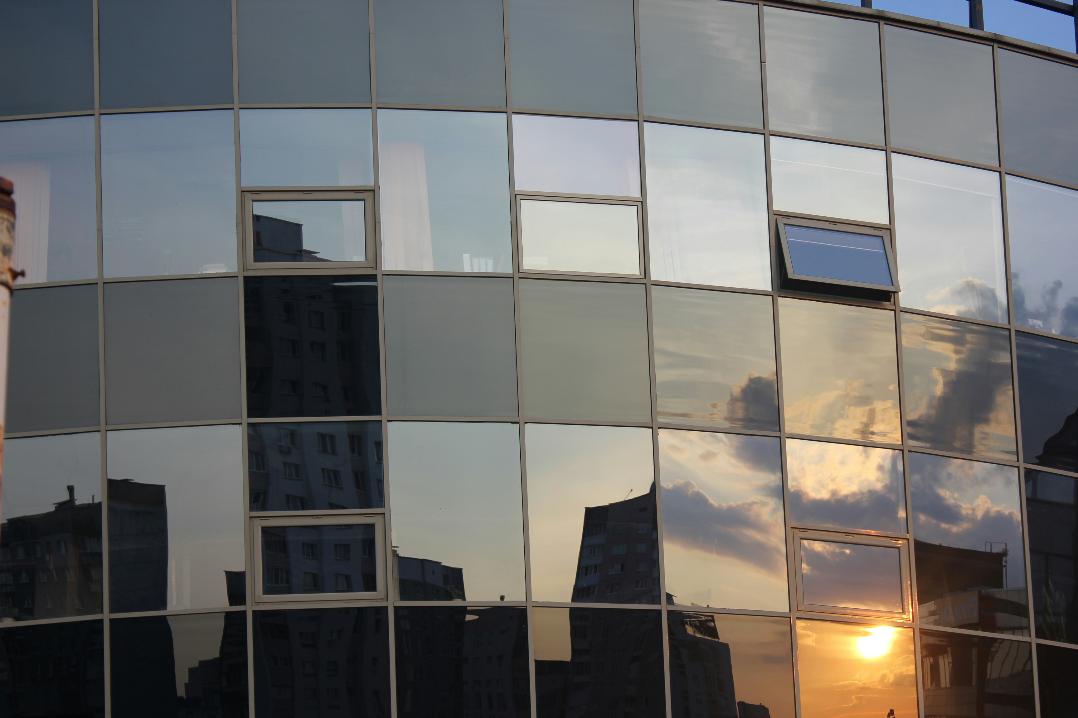 Building windows reflecting a colorful sunset with scattered clouds.