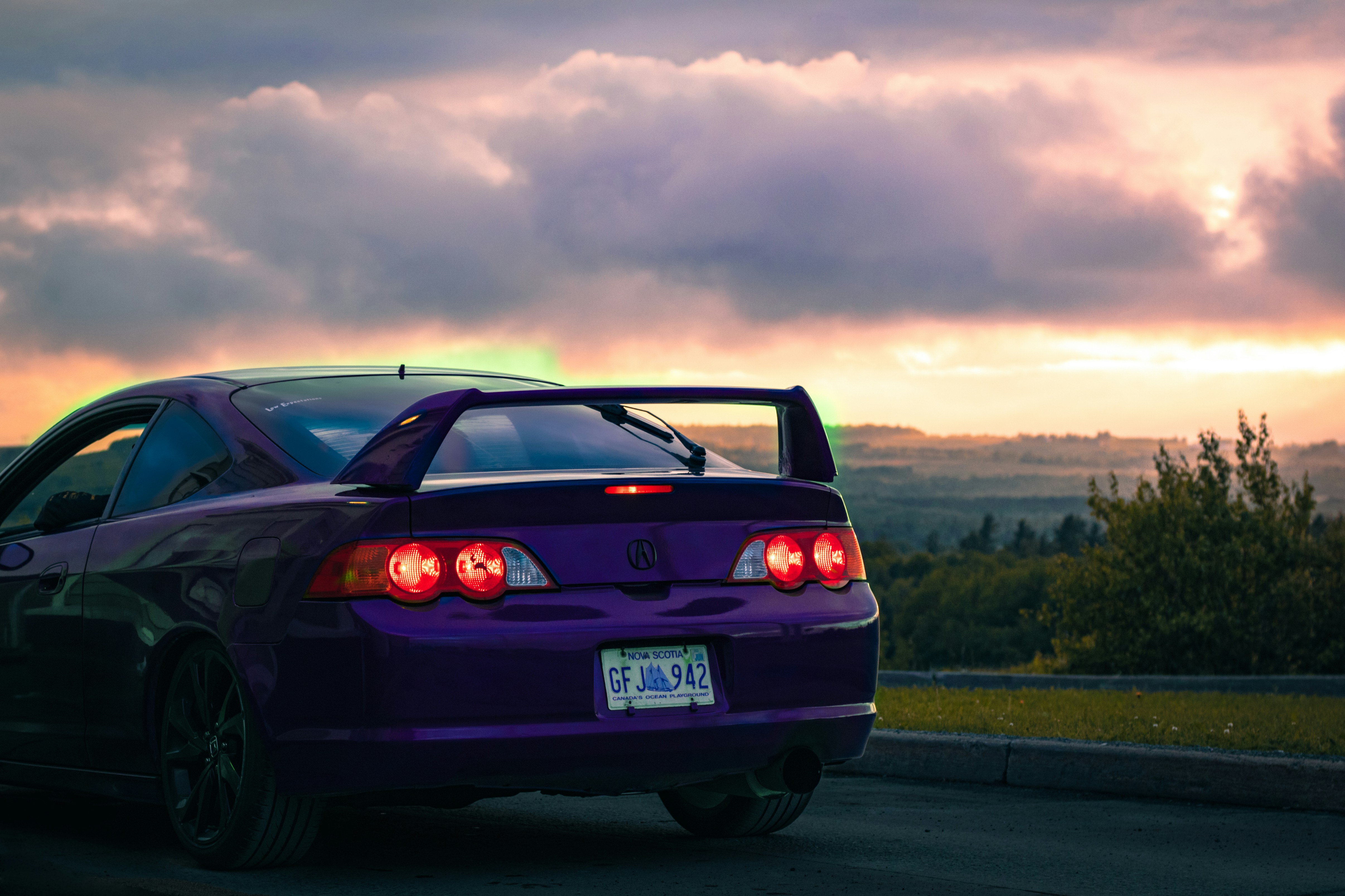 Purple sports car parked by the roadside with a dramatic sunset backdrop, showcasing vibrant colors and serene landscapes.