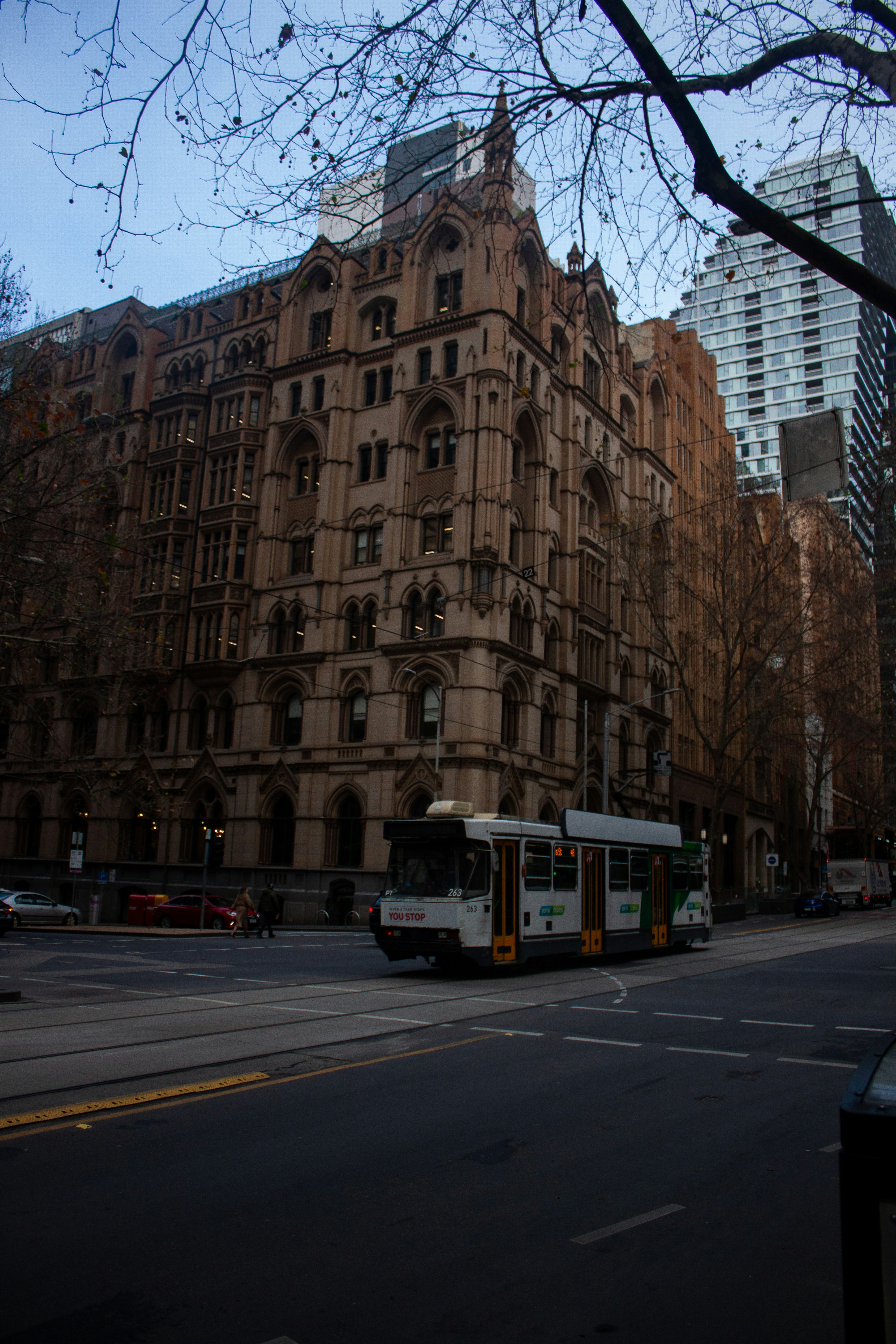 Tram Glide by a Gothic Revival Brick Facade on a Tree-Lined City Street