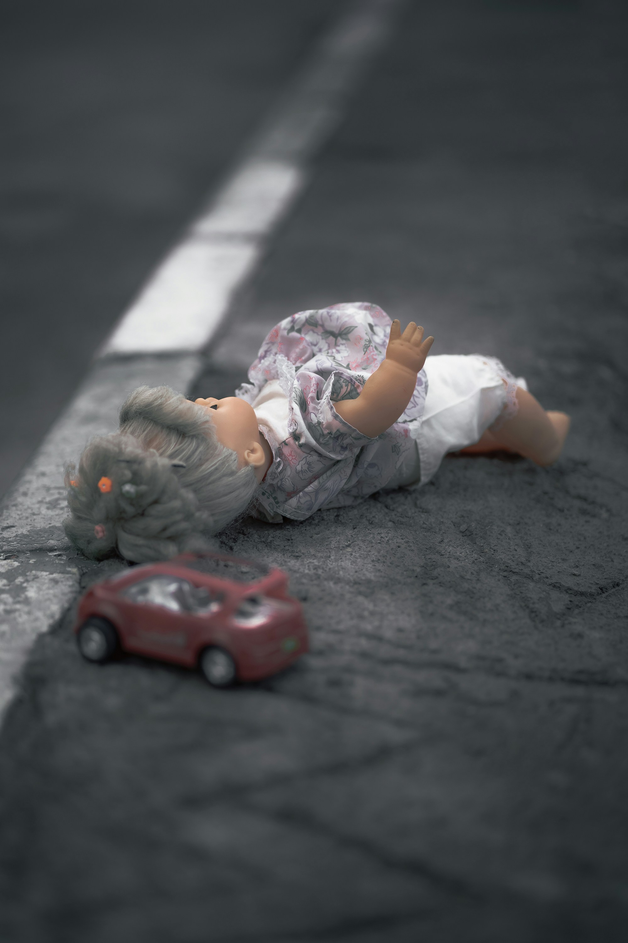 Doll on the Asphalt Line: A Quiet Street Moment with a Red Toy Car