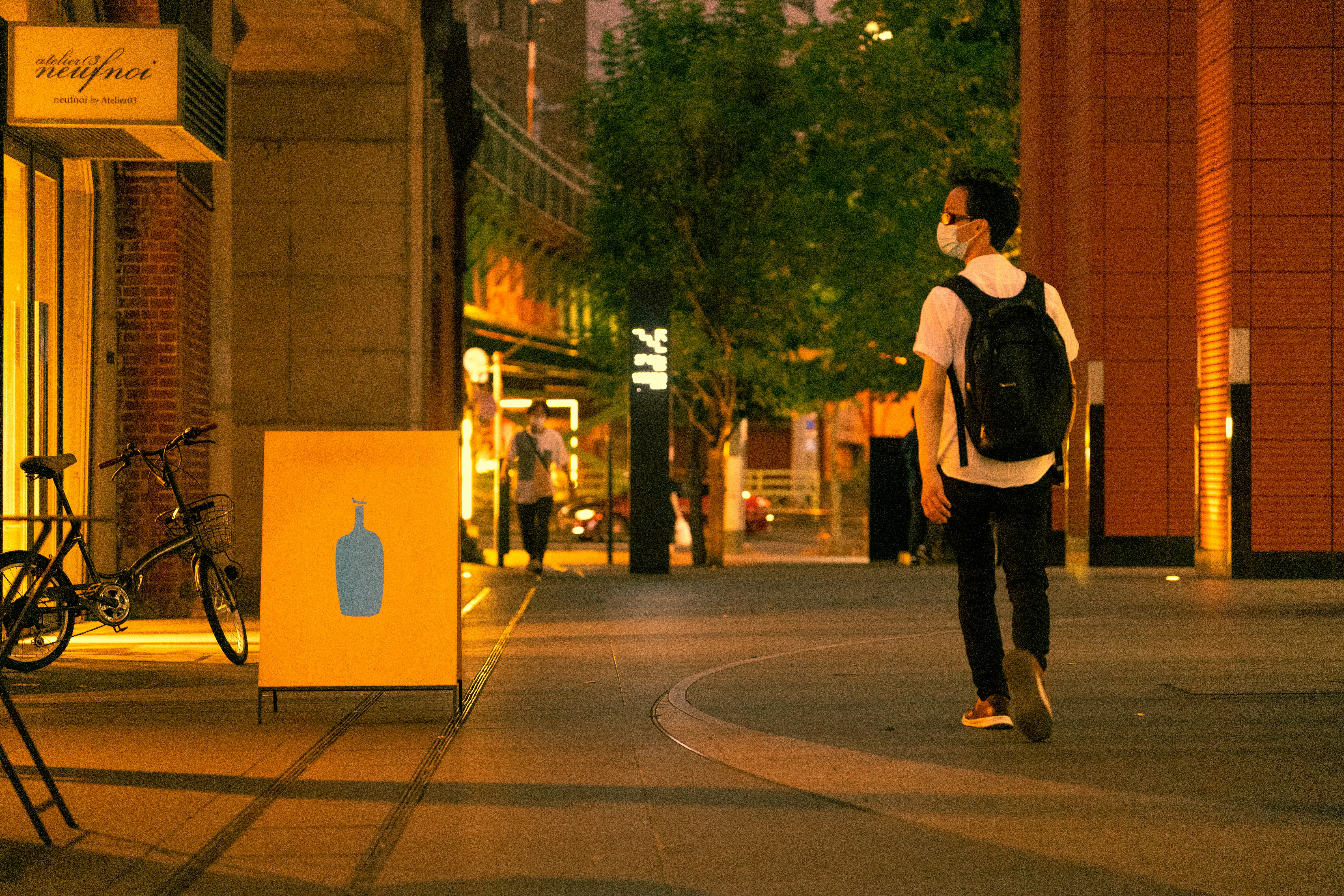 Amber Night Stroll: A Masked Pedestrian in a Quiet City Block
