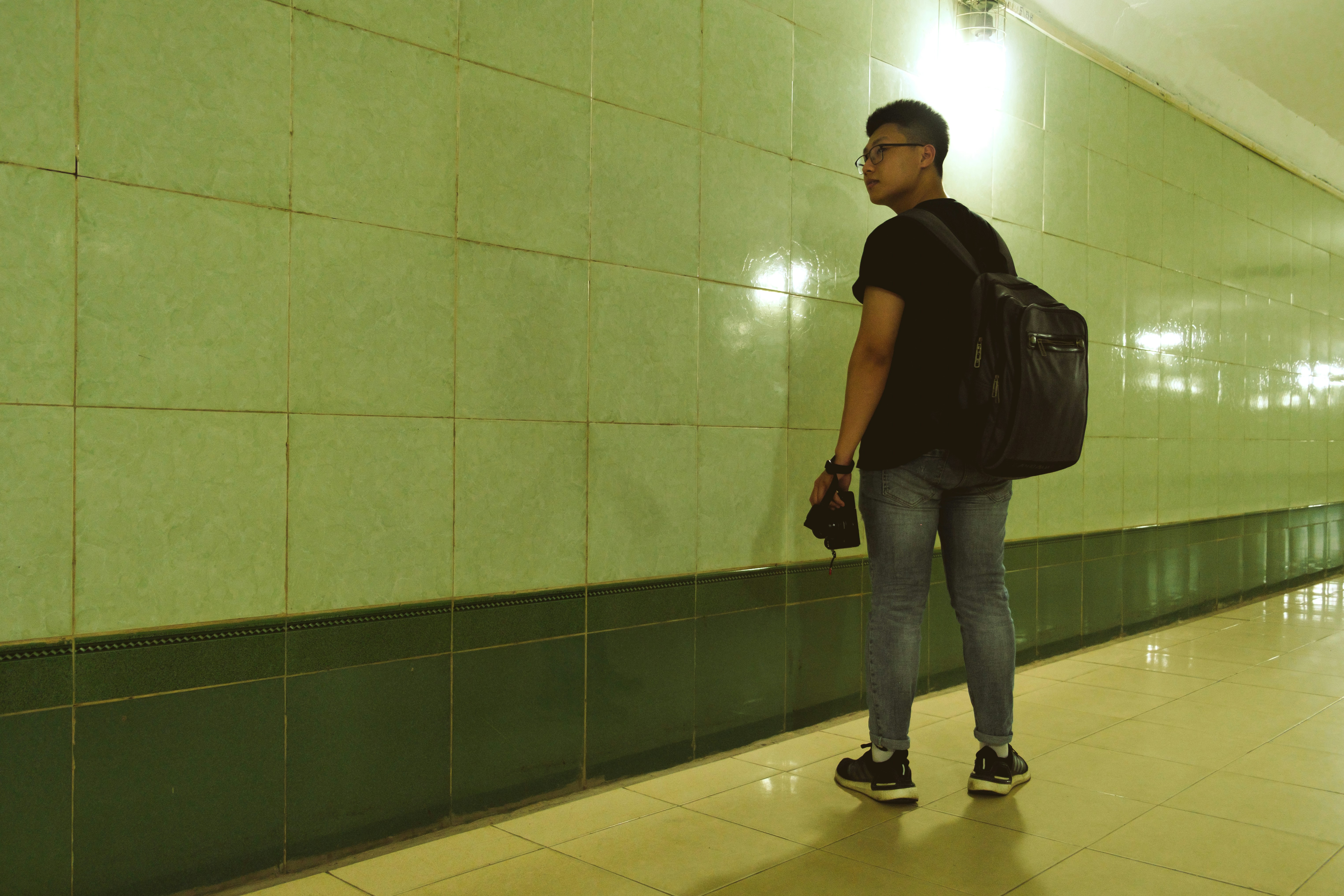 A person stands in a dimly lit subway corridor, gazing thoughtfully at the tiled wall, evoking a sense of urban solitude.