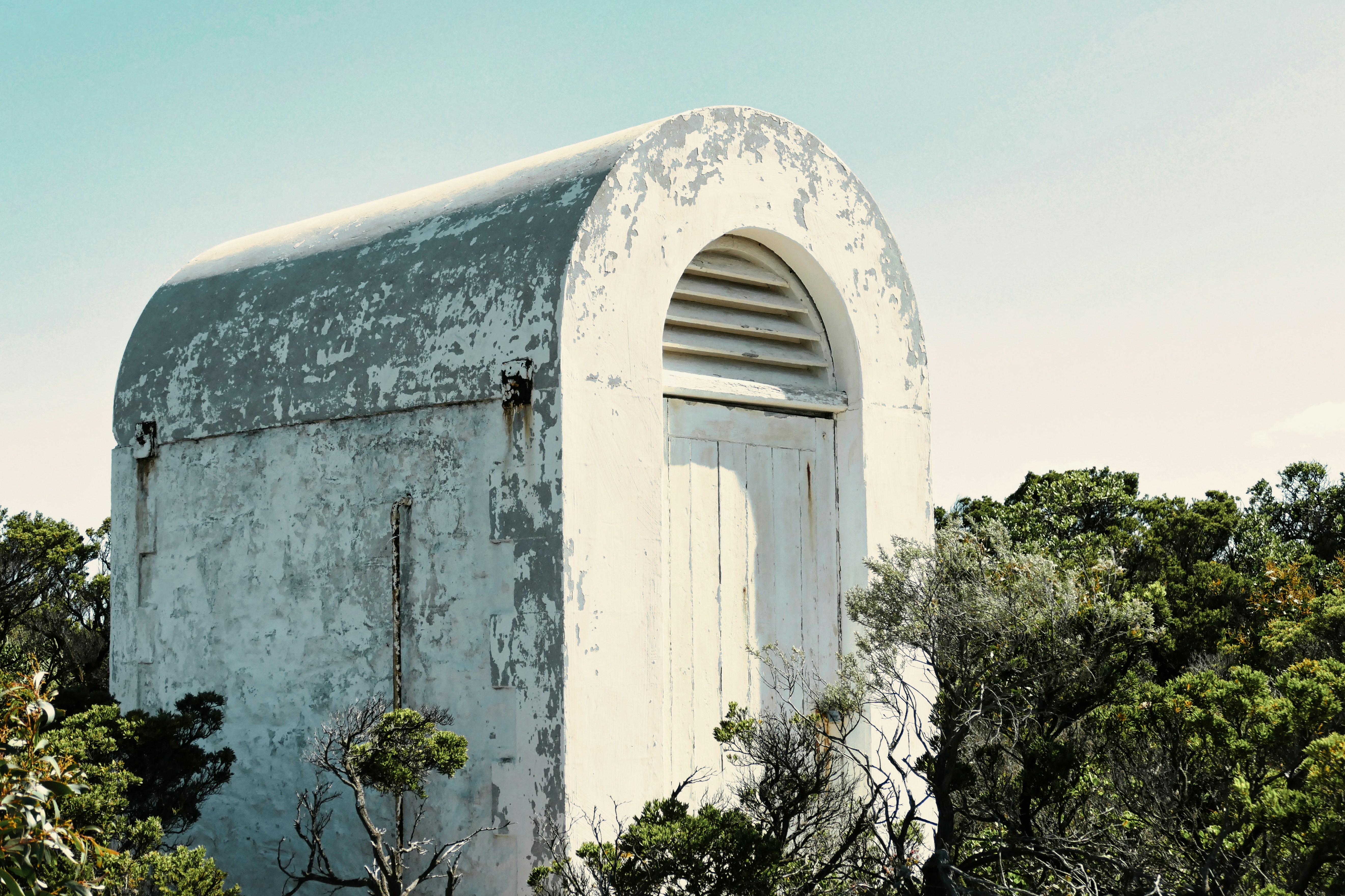 Weathered Niche: A Desaturated Teardrop Hut Rising from Scrub