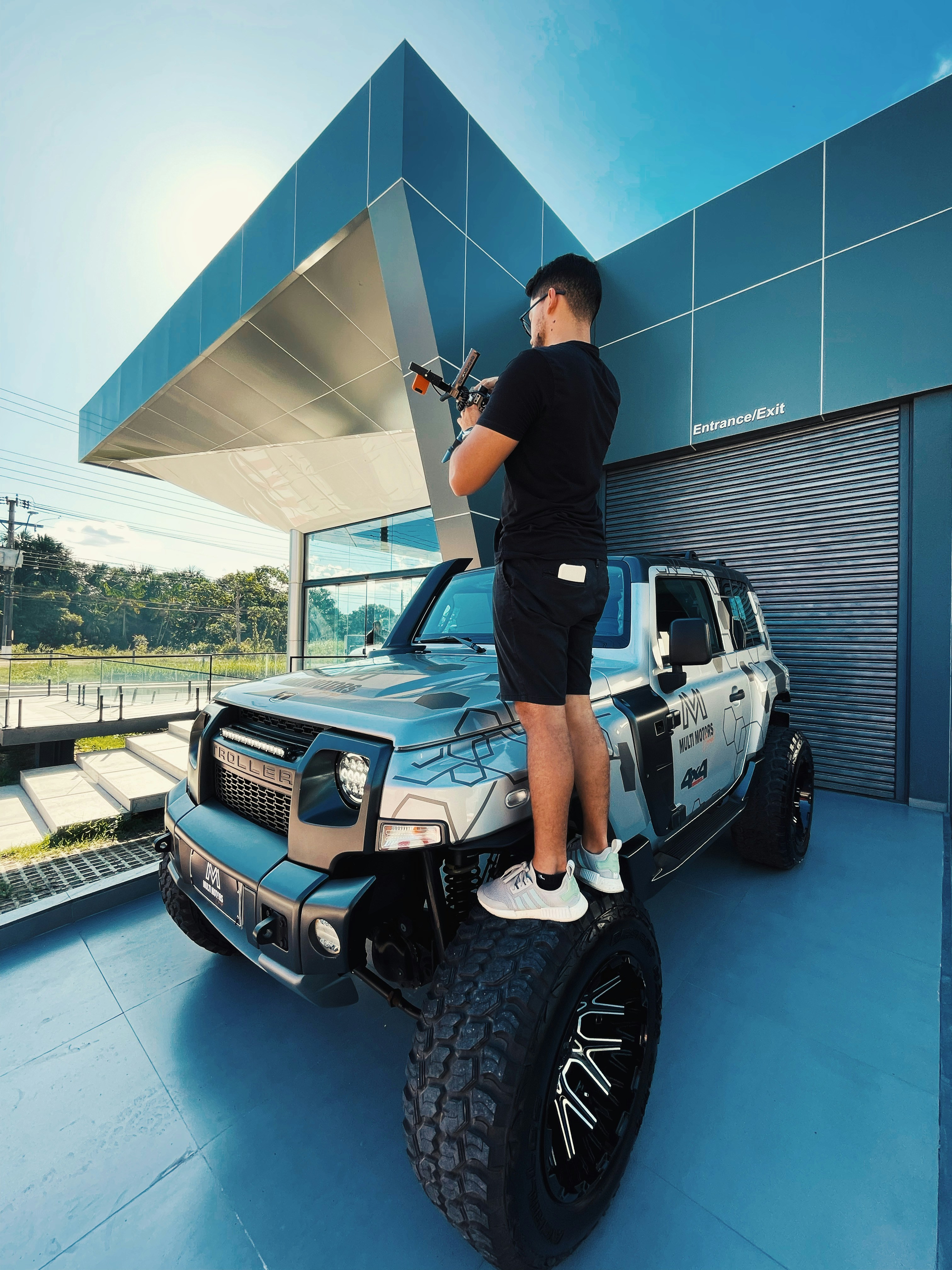 Edge of Elevation: A climber surveys a chrome monster truck at a glossy showroom exterior