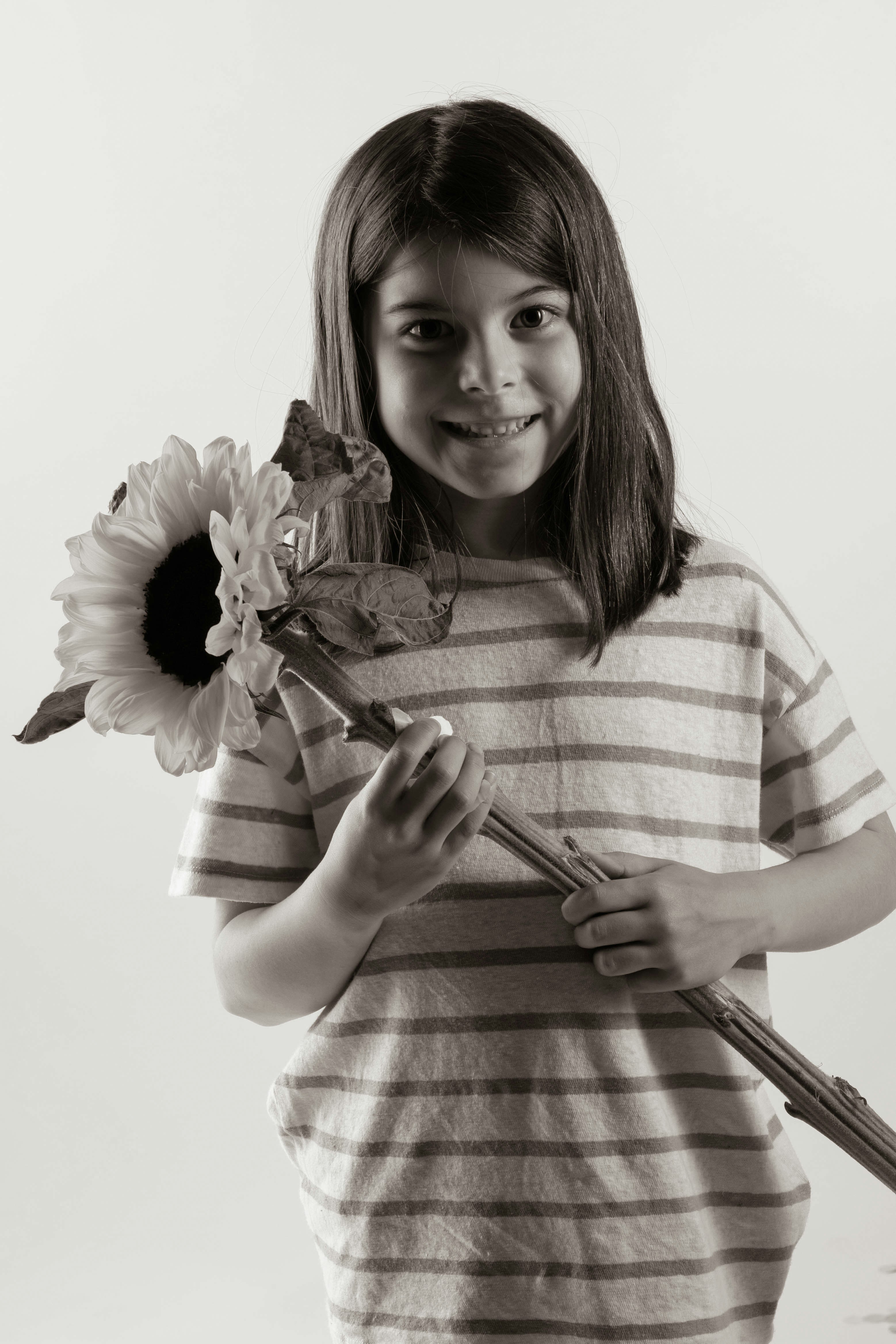 Young girl holding a sunflower, radiating happiness in a minimalist setting.