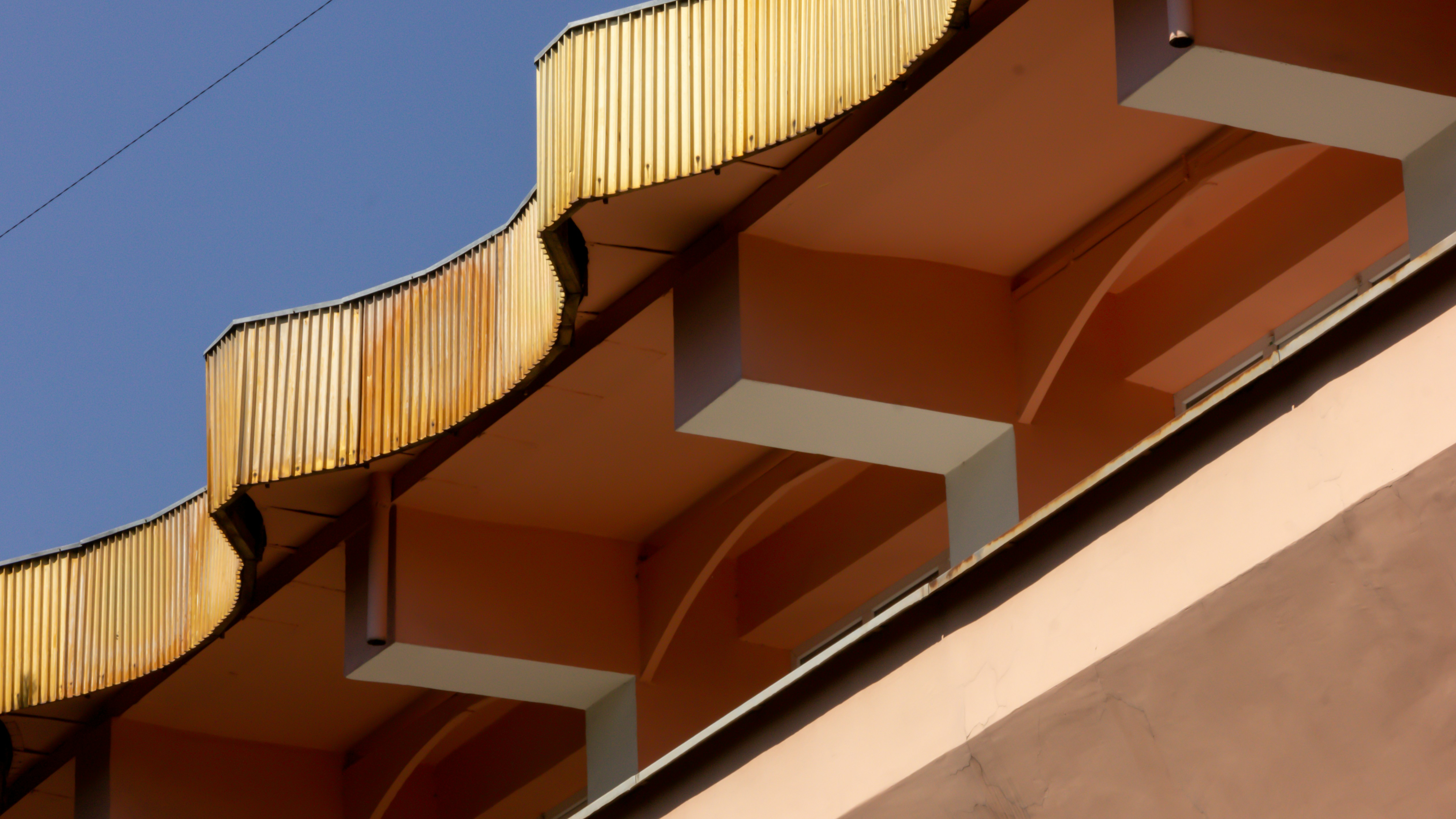 Curved metal awning casts shadows on a pastel-colored wall, showcasing a blend of architectural elements and textures.