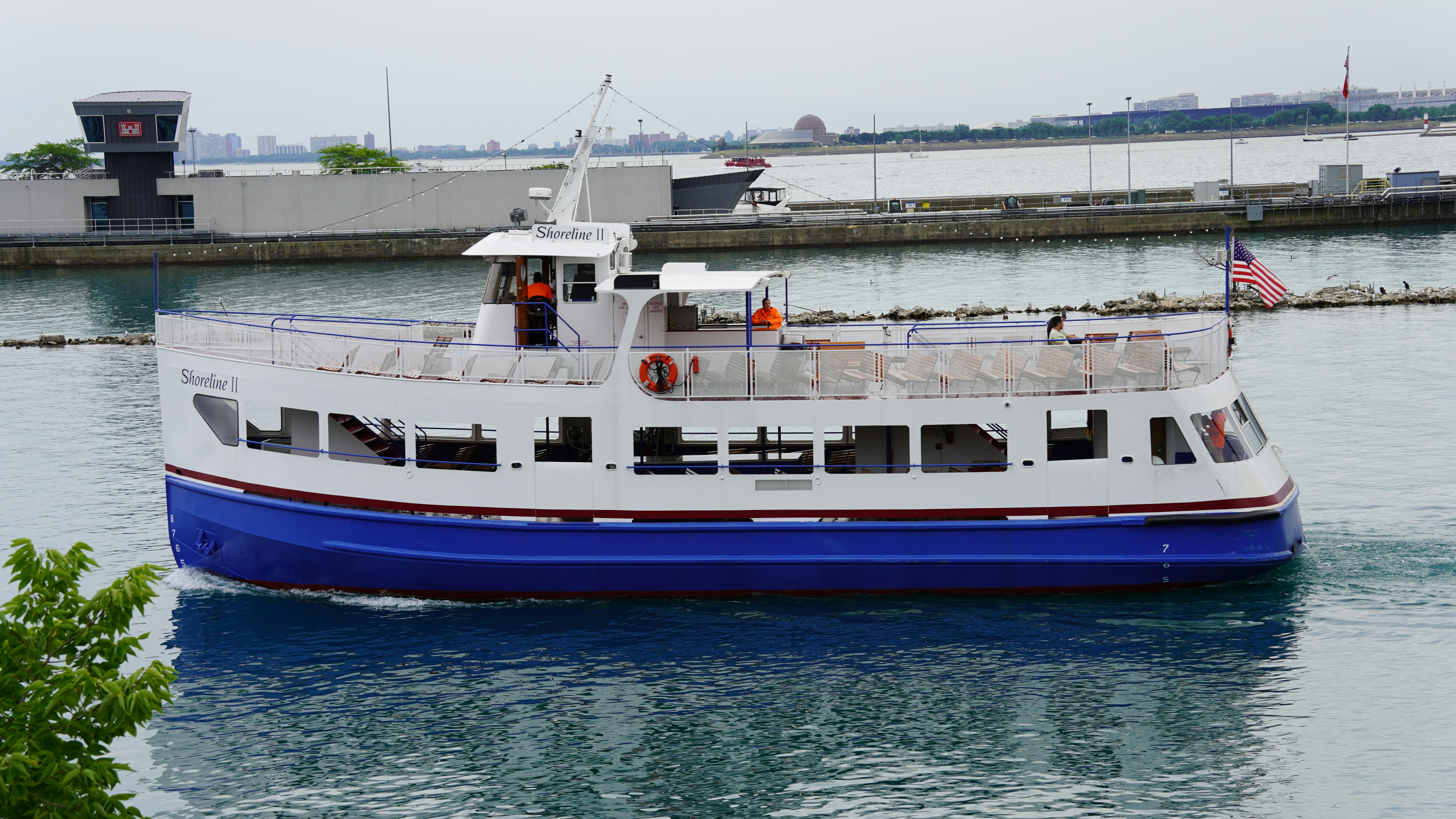 A ferry gliding through tranquil waters, showcasing its sleek design against a backdrop of cityscape and greenery.