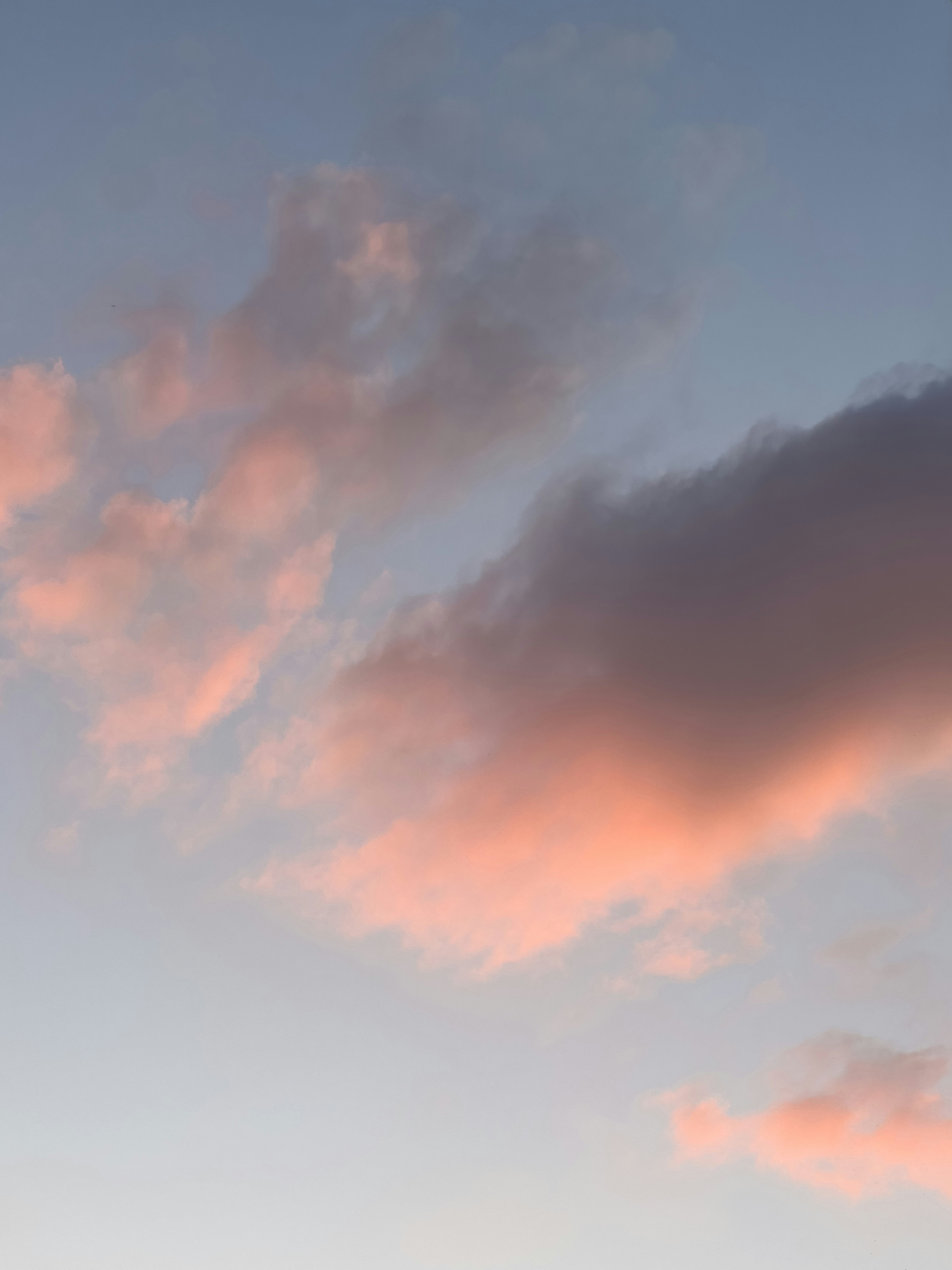 Soft pink and white clouds drift across a serene blue sky at dawn.