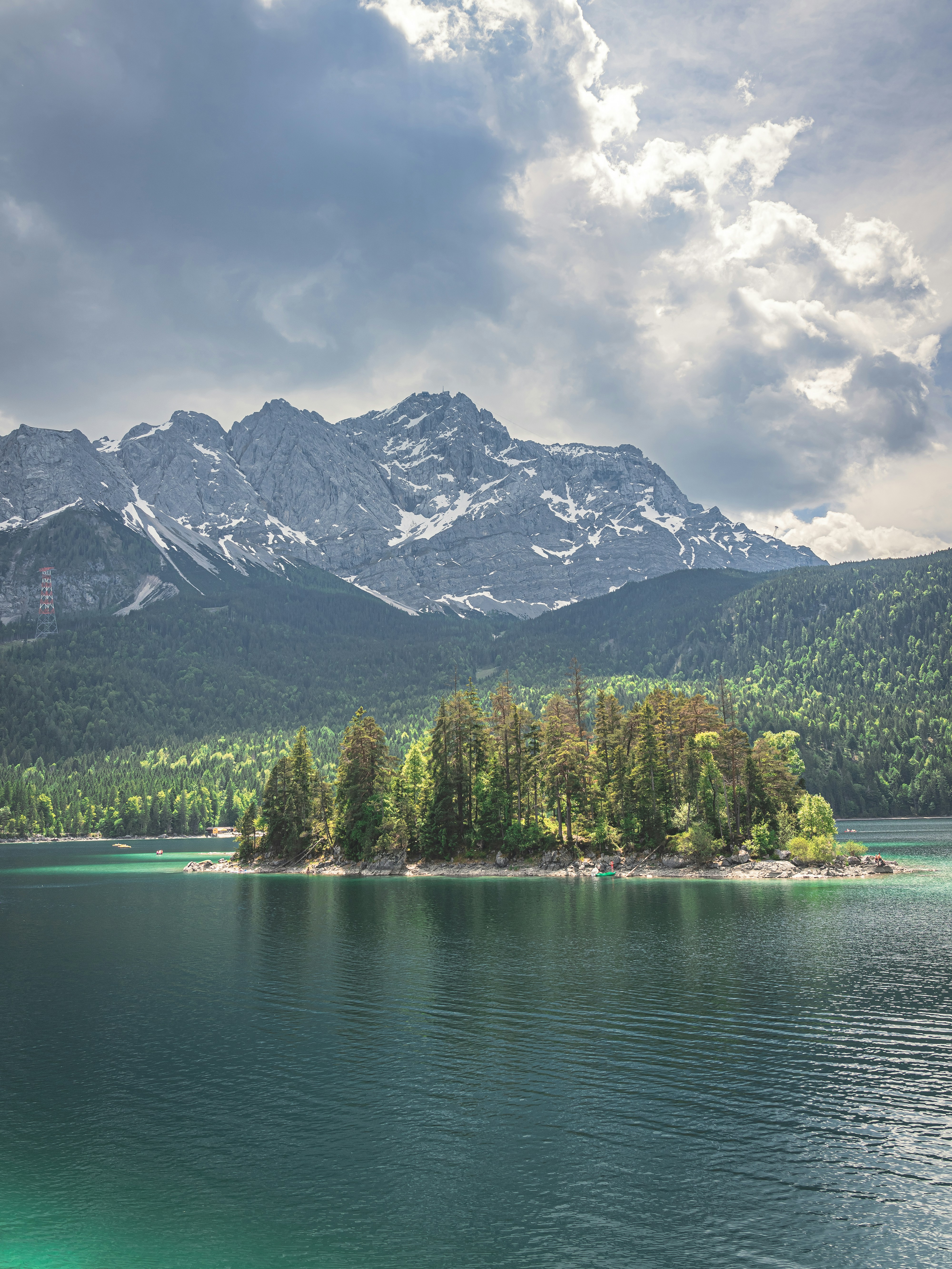 Lush island surrounded by tranquil waters and towering mountains under a dramatic sky.