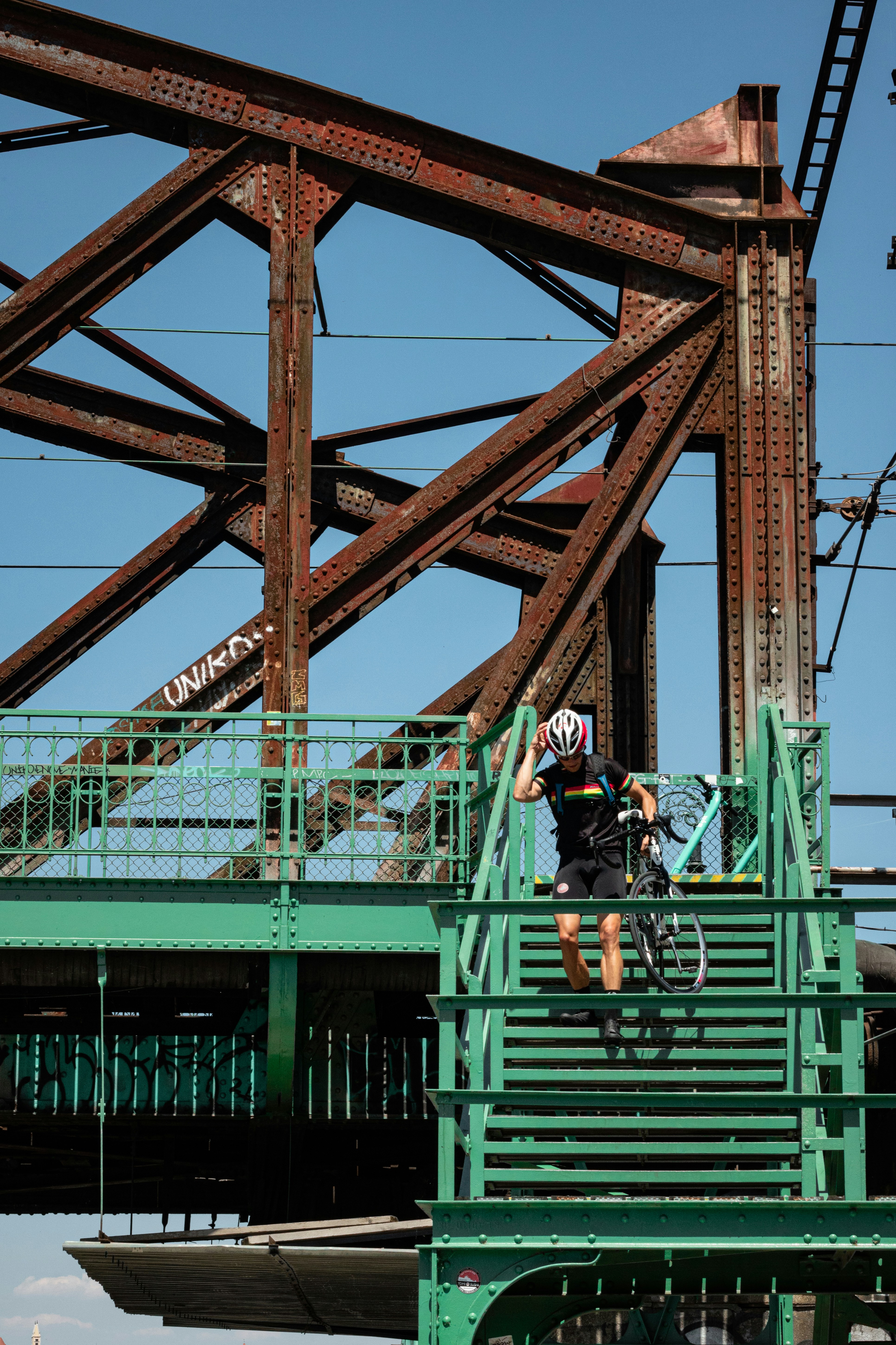 Beneath the Rusted Span: A Cyclist Pauses on a Green Stairway