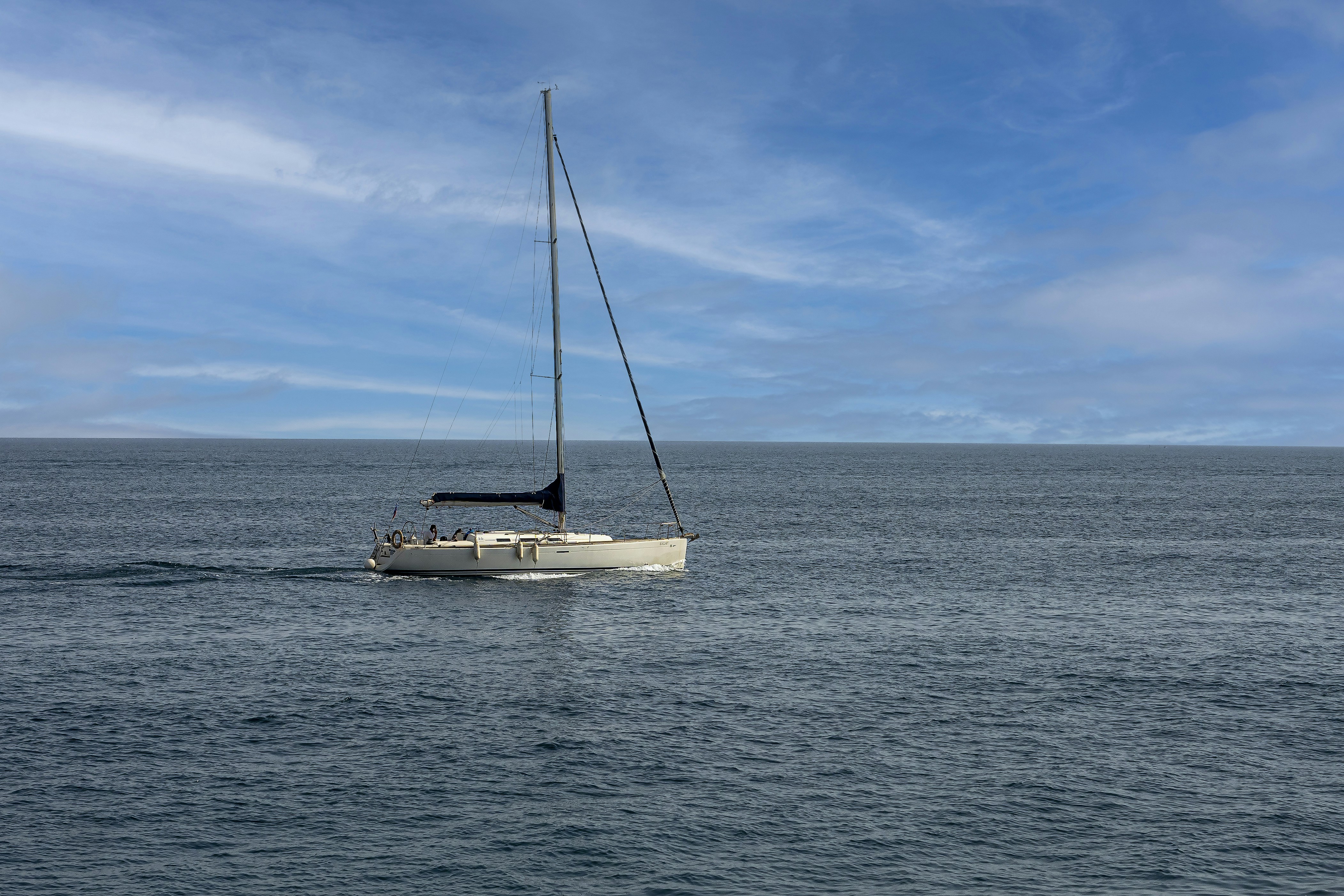Sailboat gliding smoothly across the calm sea under a vast, cloudy sky.
