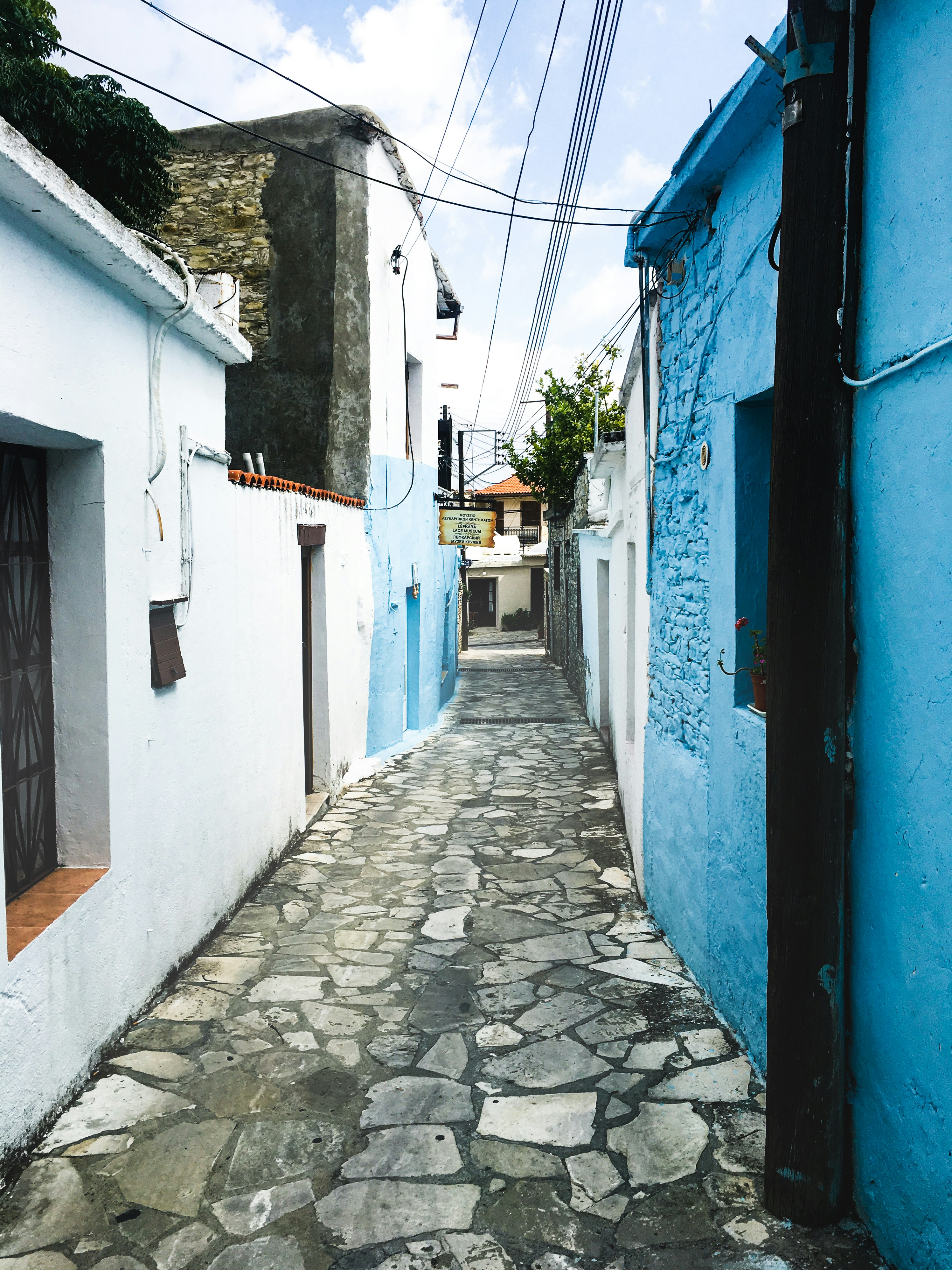 Narrow stone pathway flanked by vibrant blue and white buildings under a partly cloudy sky.