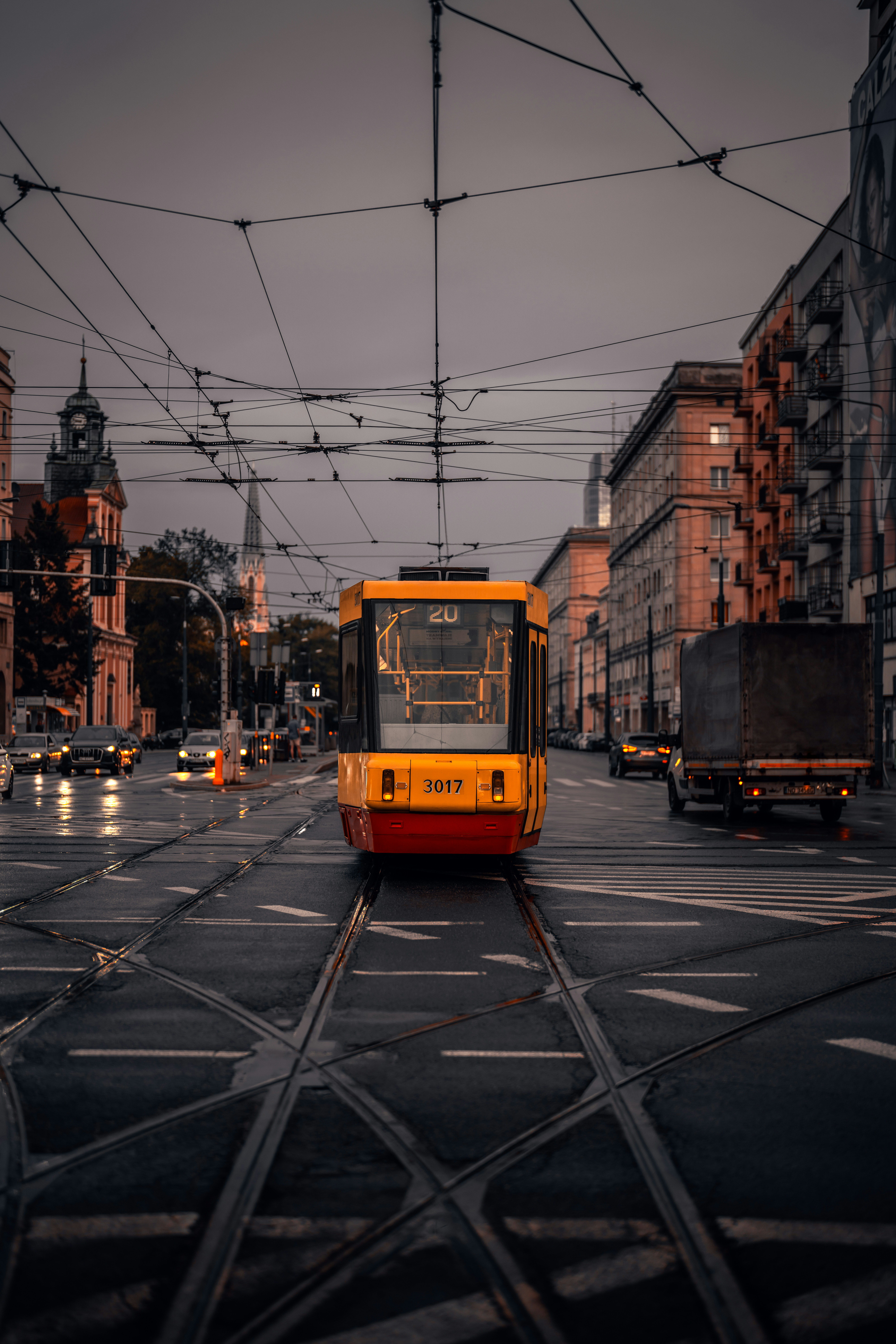 Tram navigating through a rain-soaked urban street, surrounded by historic architecture and illuminated by streetlights.