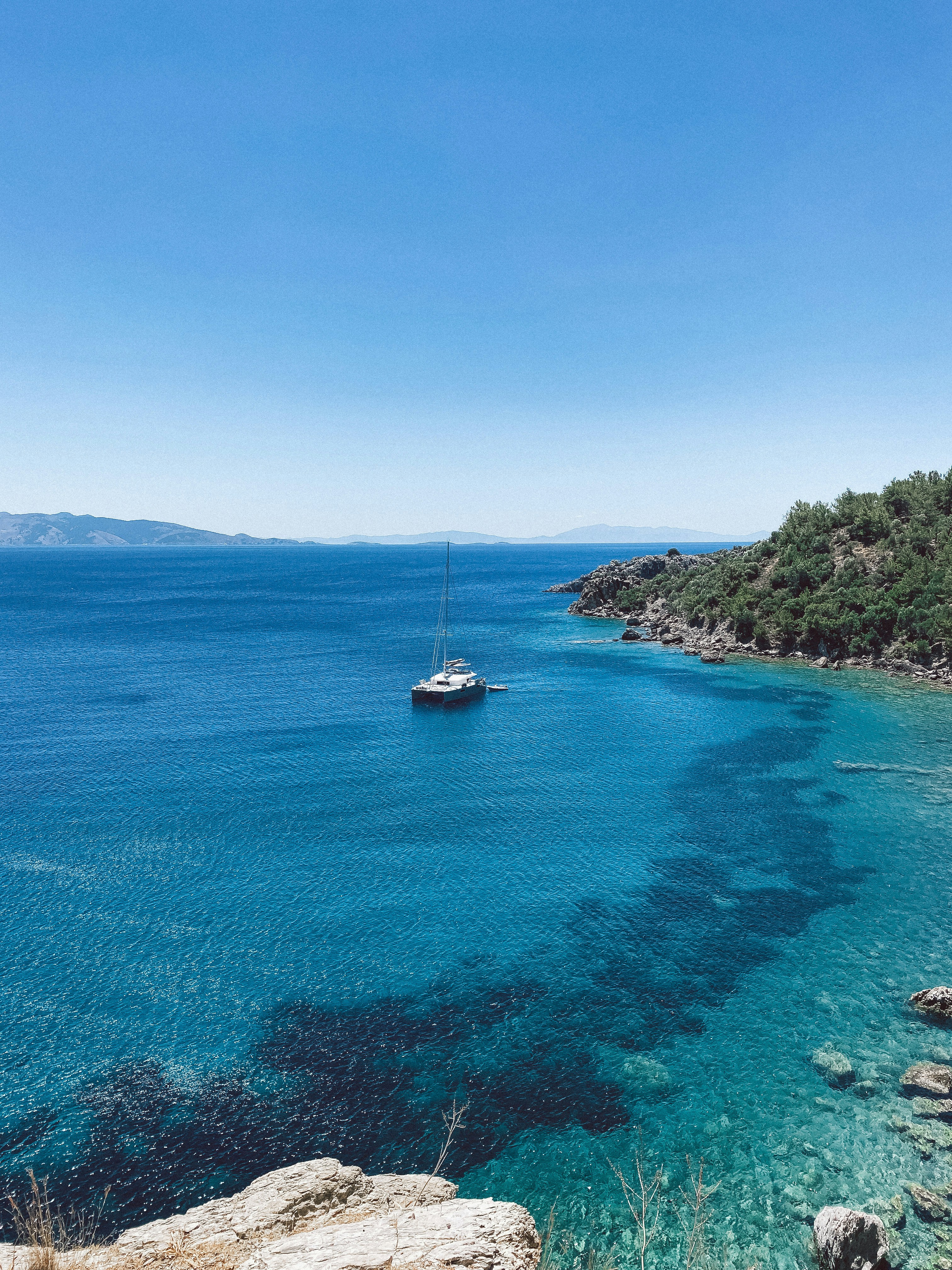 Sapphire Quiet: A Sailboat Drifts Along a Turquoise Cove