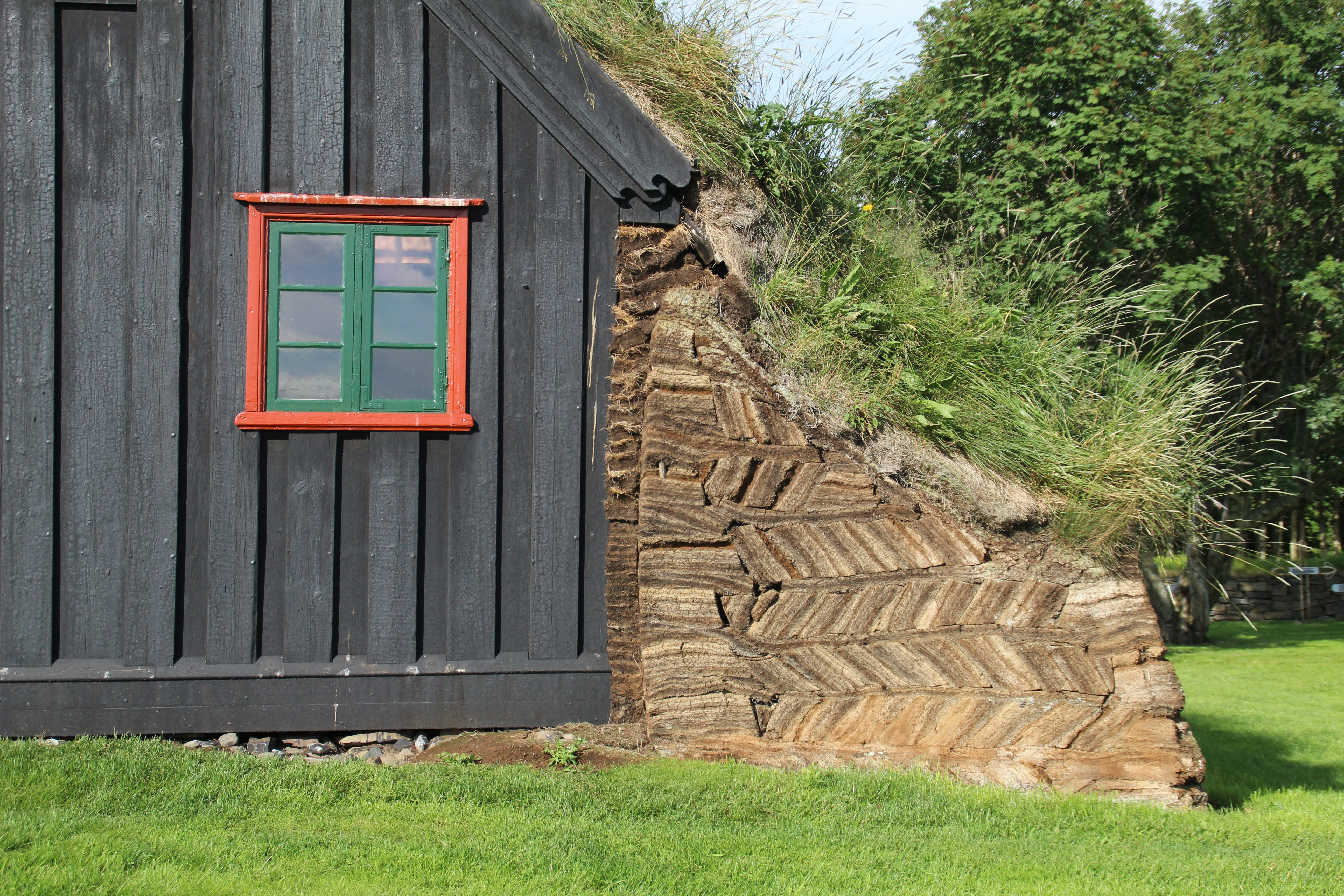 Red-Framed Window Anchors a Timber Cottage Beside a Terraced Earthen Bank