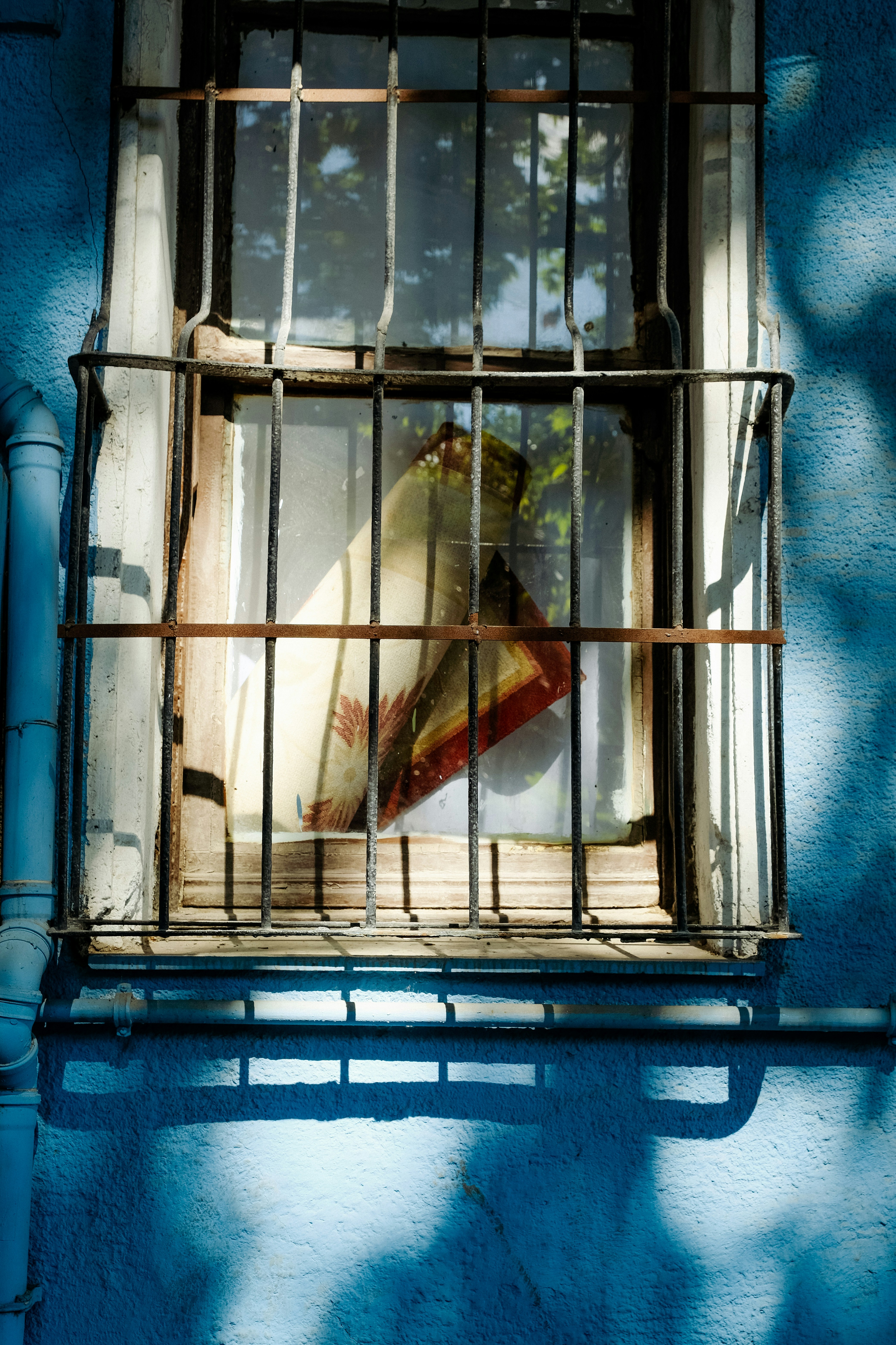 Azure Facade Behind Grilles: Sunlit Window on a Blue Wall