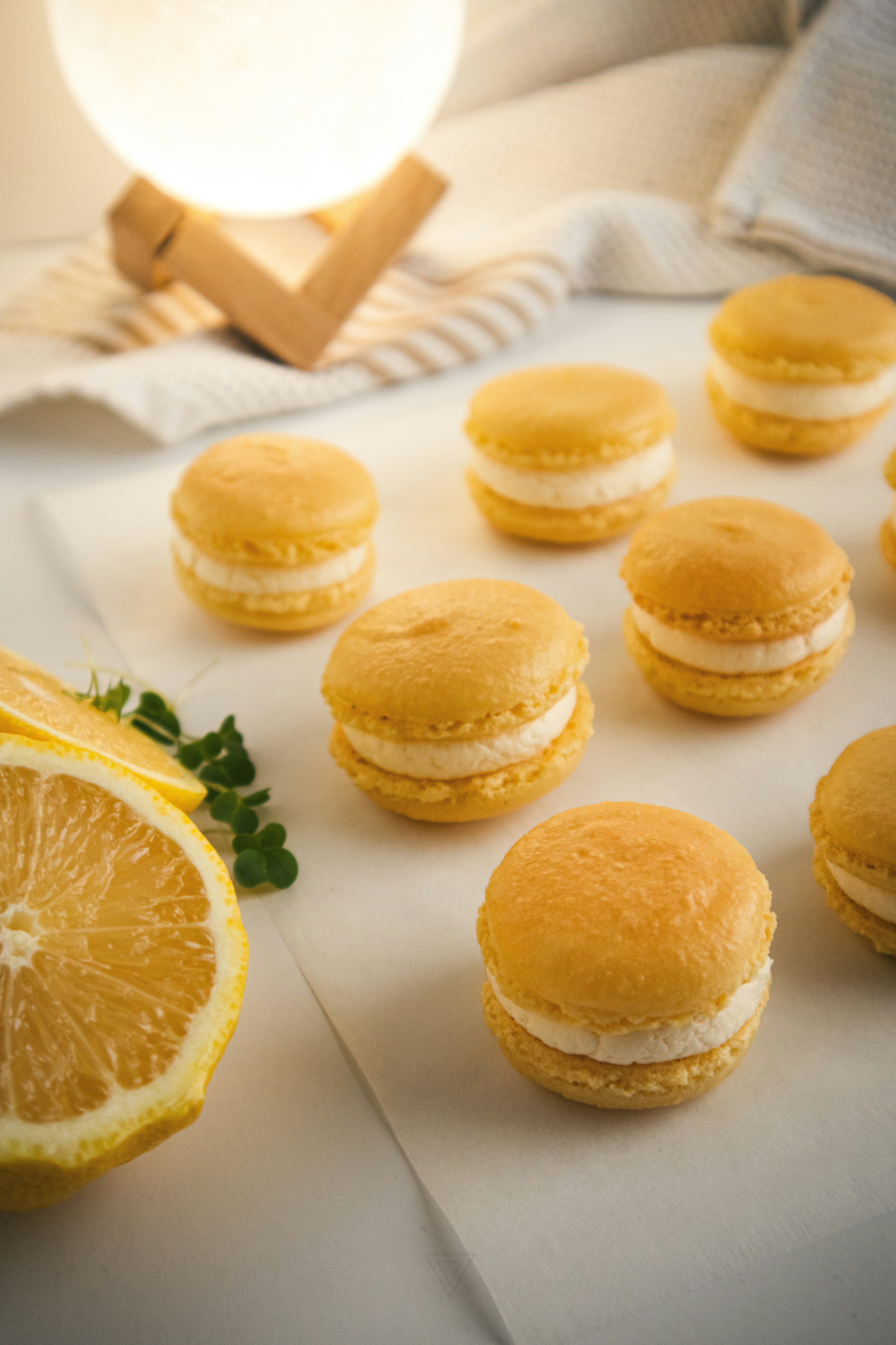 Lemon macarons arranged on a white surface with sliced lemon and soft lighting.