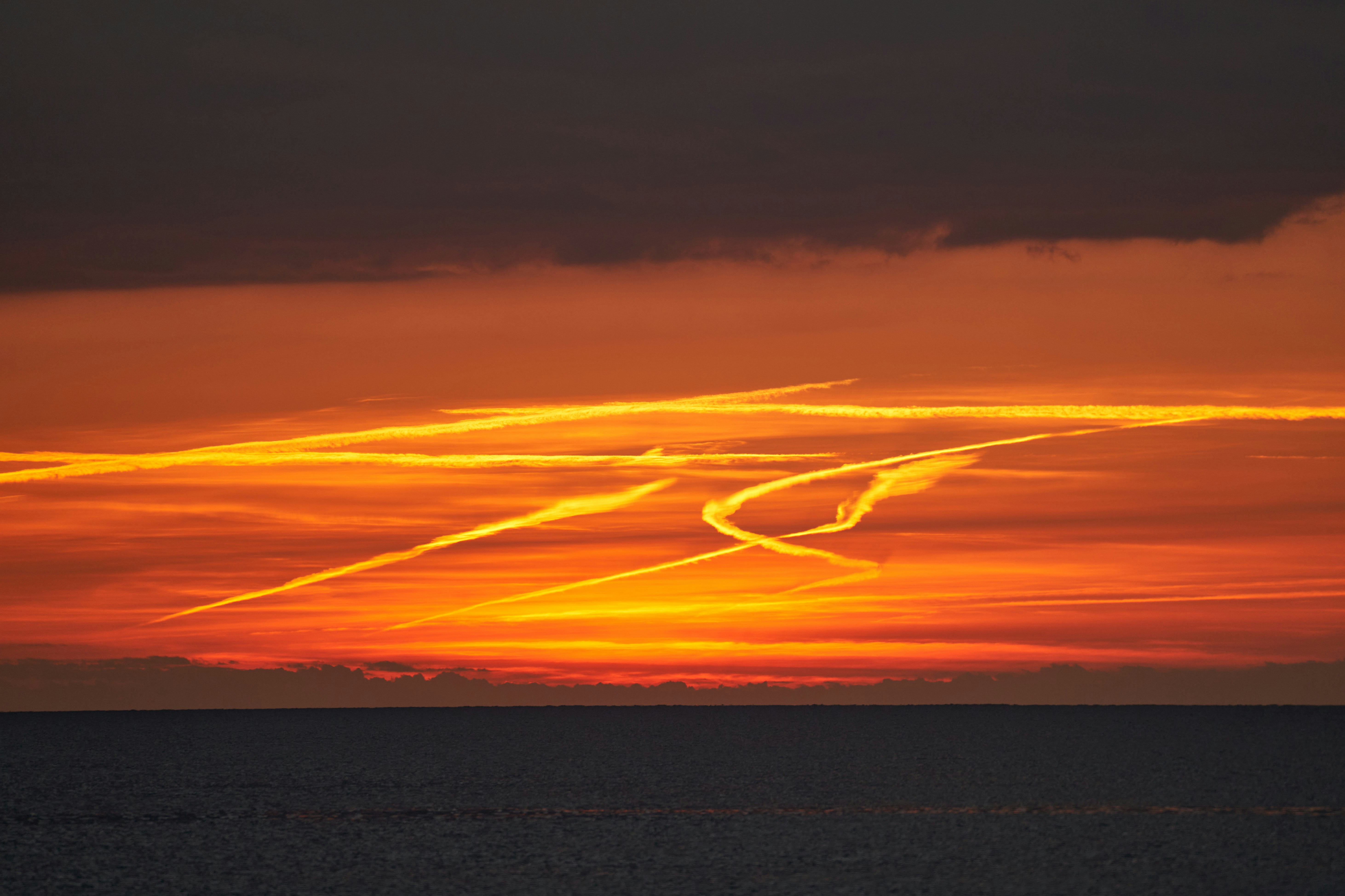 Crimson Contrails at Dusk: Ocean Horizon Painted in Light