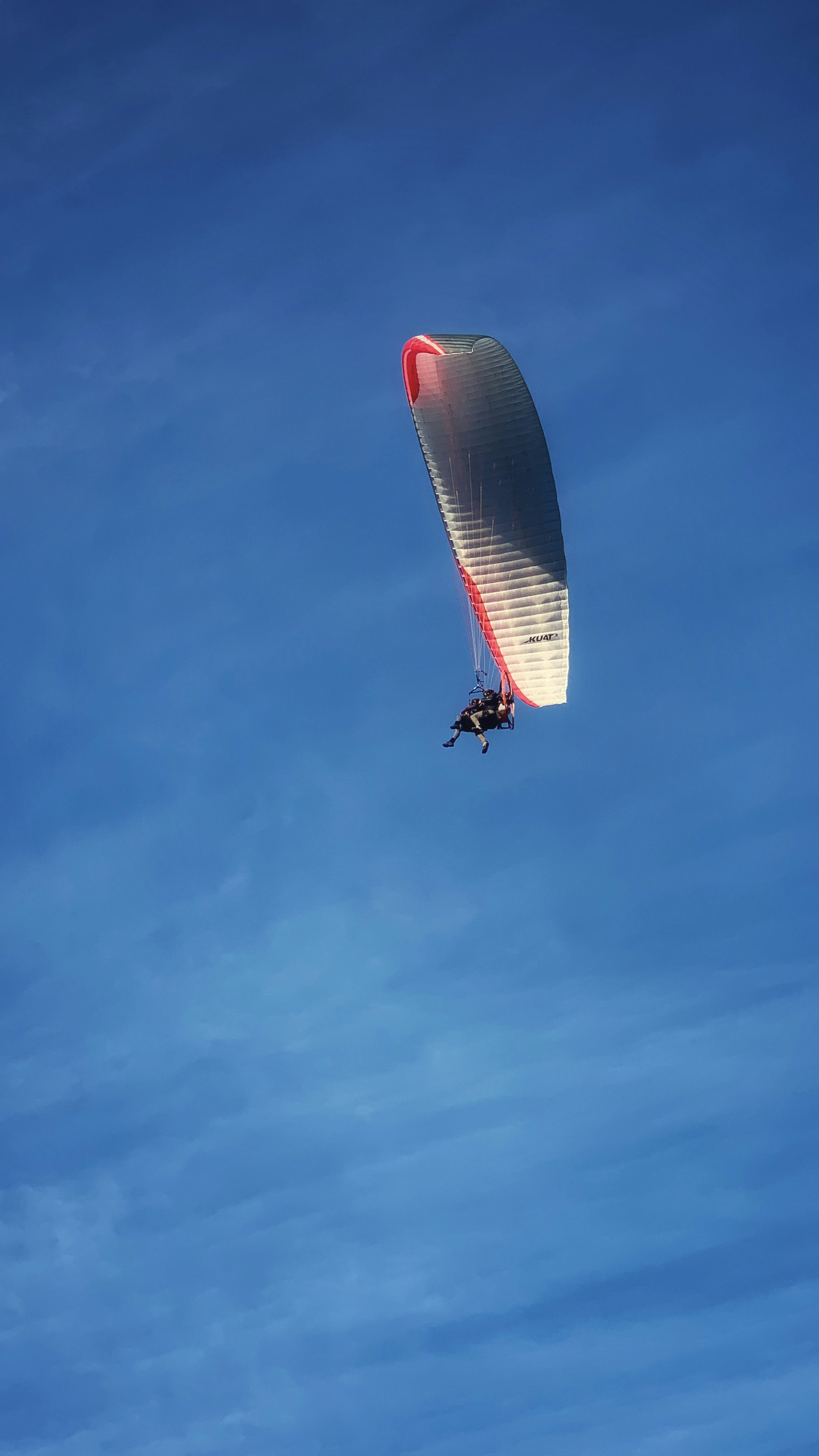 Red-Edged Tandem Paraglider Cutting Across a Cerulean Sky