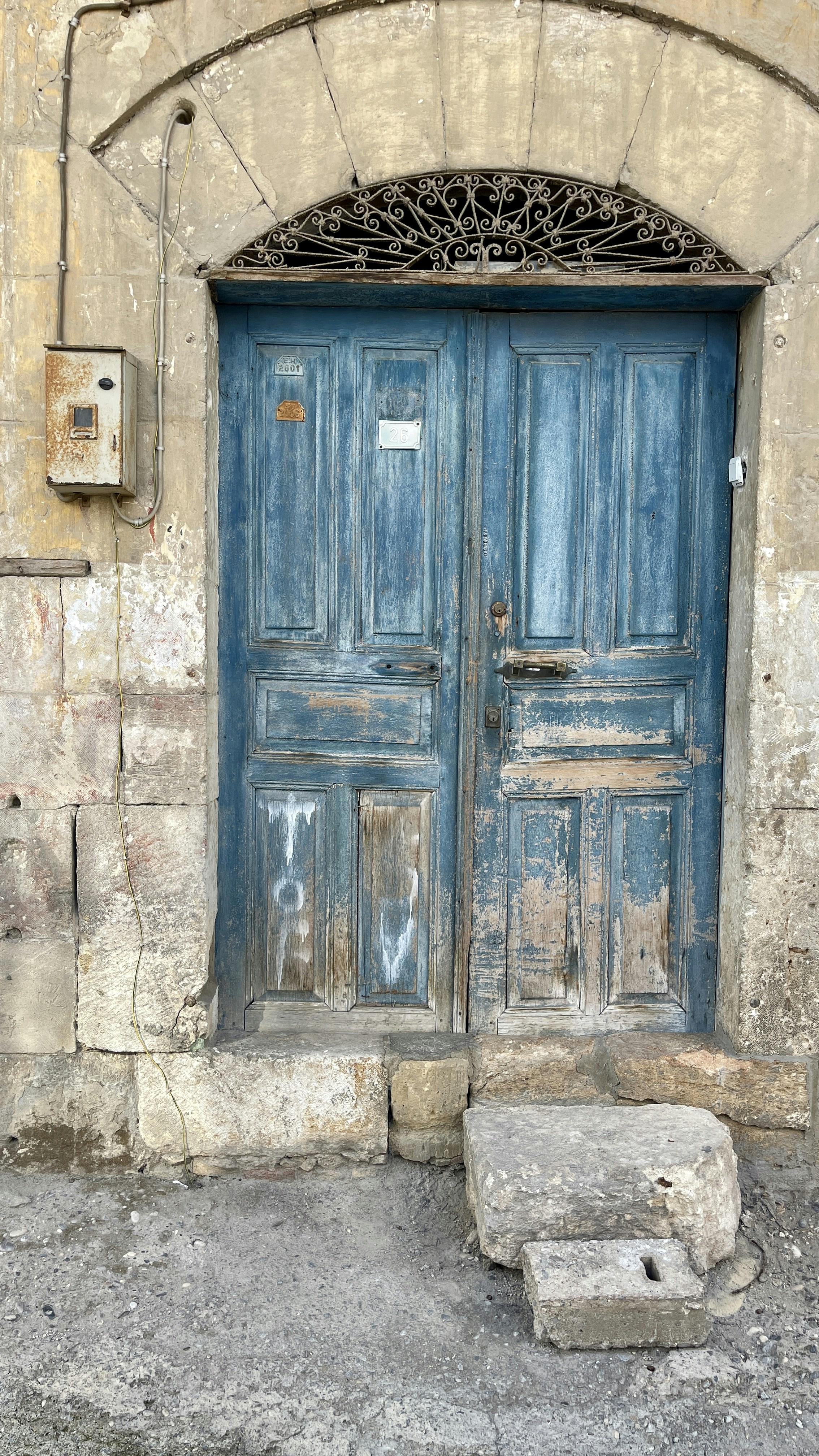 A rustic blue door with peeling paint set in a stone facade, featuring a decorative metal grille above.