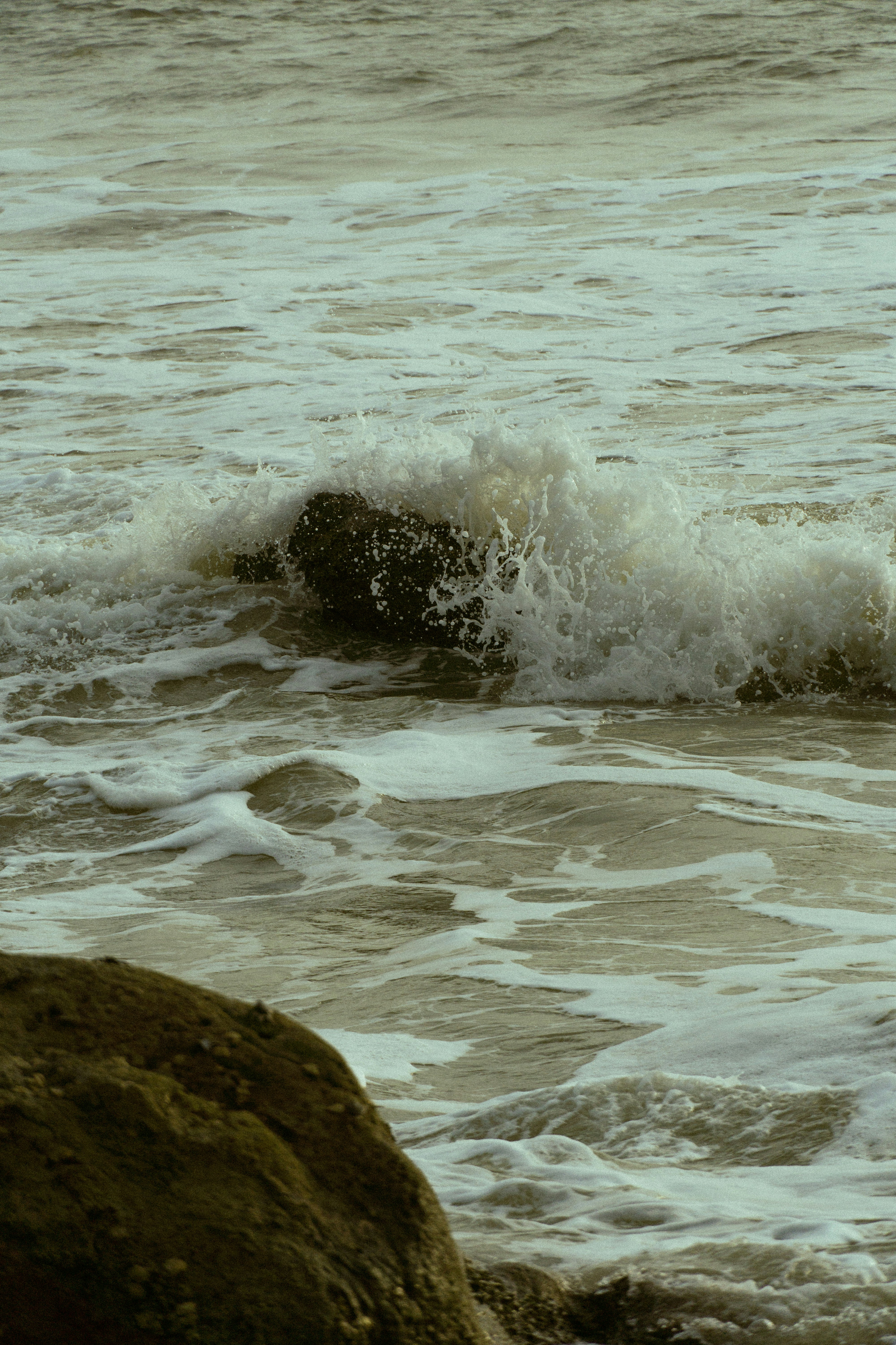 Gentle waves caress a rugged rock as the tide ebbs and flows, capturing the serene rhythm of the ocean's embrace.