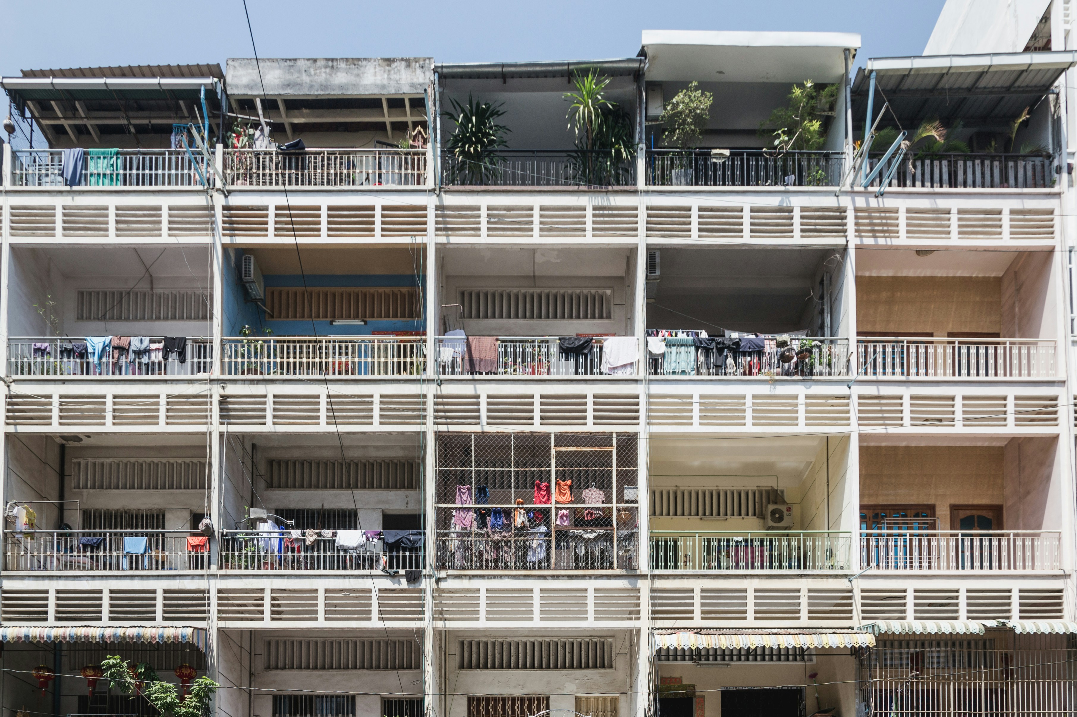 Modern building facade with multiple balconies featuring plants and everyday items.