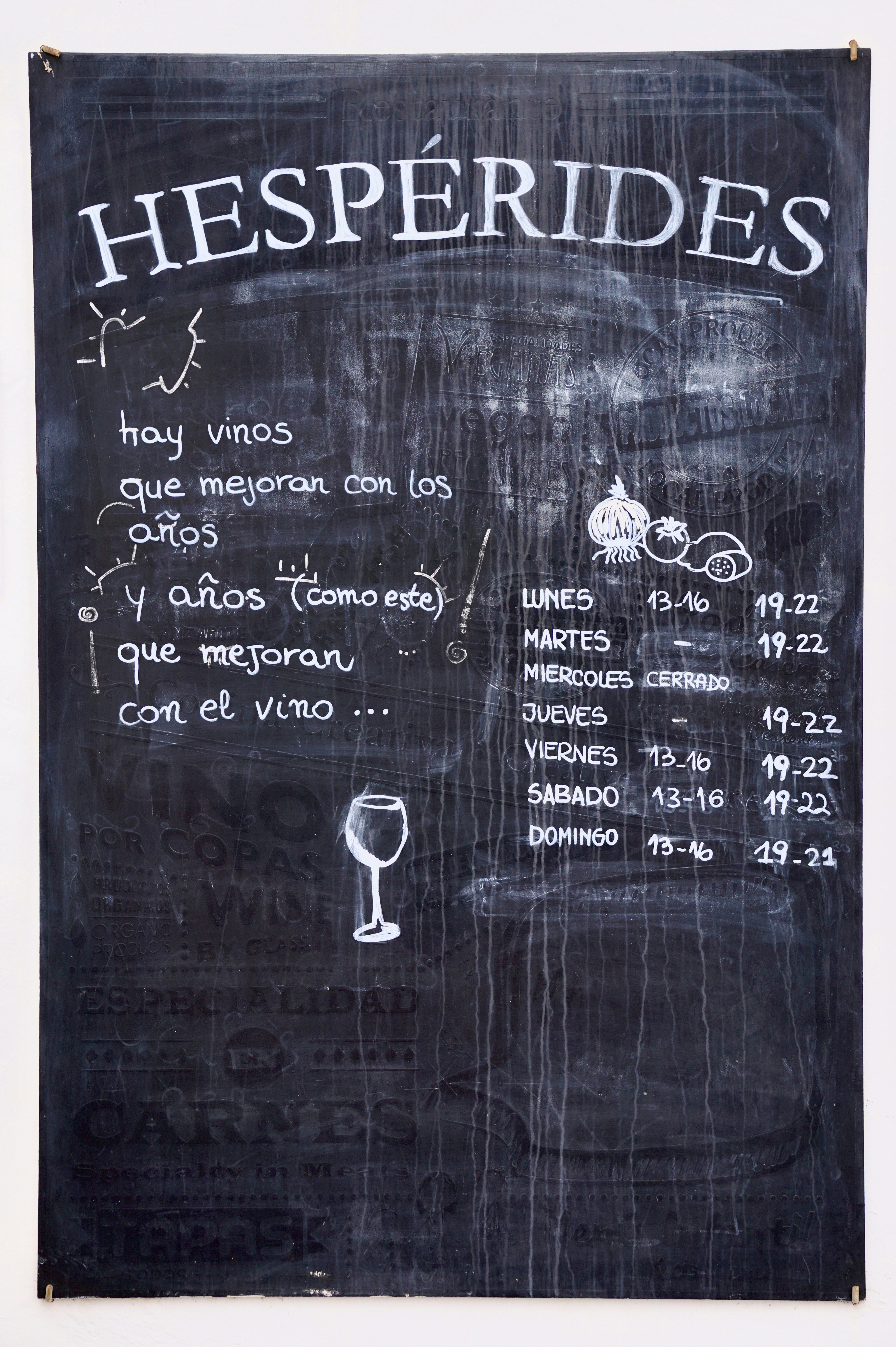 Chalkboard menu displaying wine selections and weekly hours at Hespérides, featuring artistic lettering and illustrations. A cozy atmosphere for wine enthusiasts.
