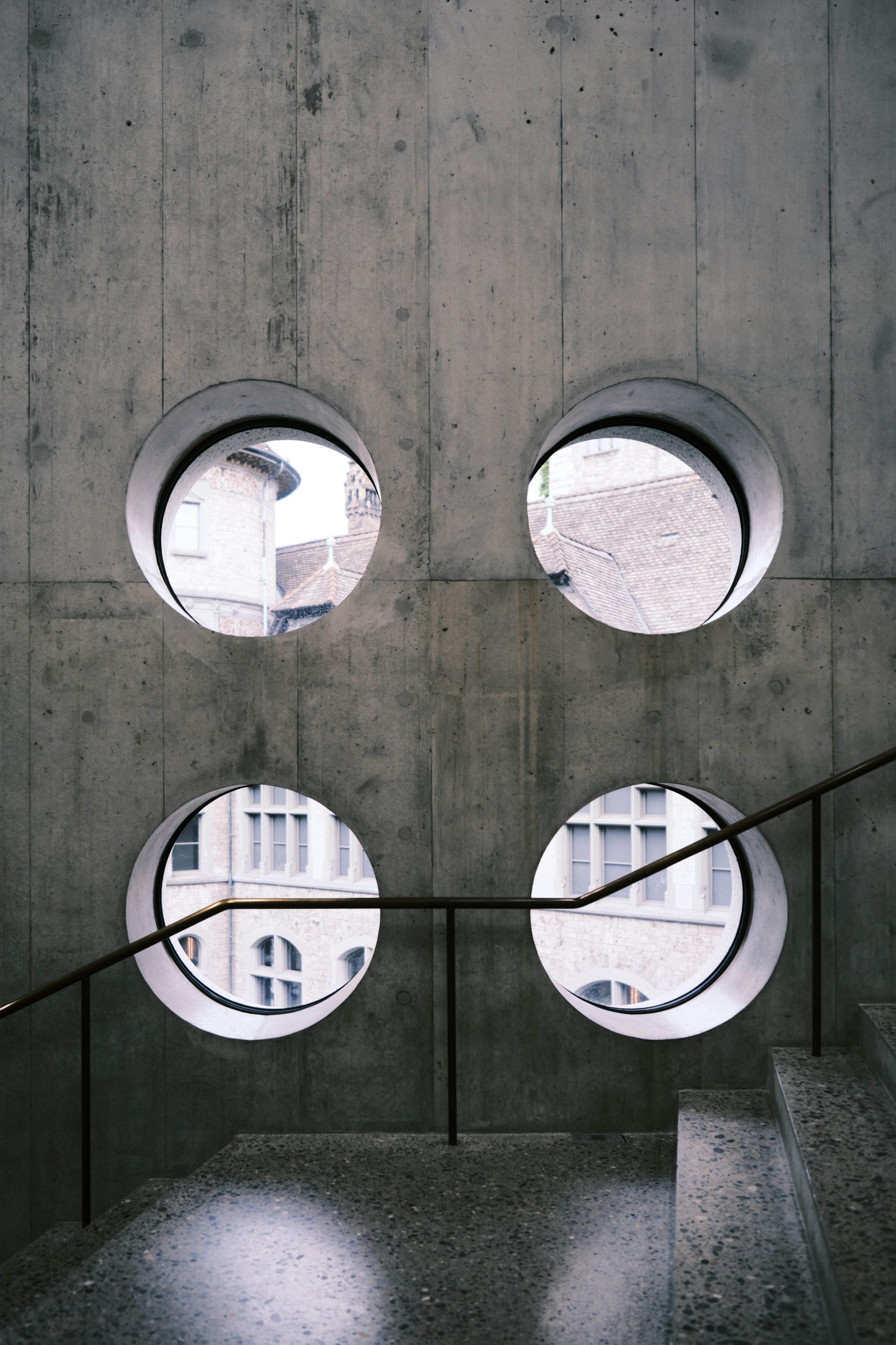 Four circular windows in a concrete wall frame a view of historic architecture outside. The interplay of modern design and classic structures creates a unique visual narrative.