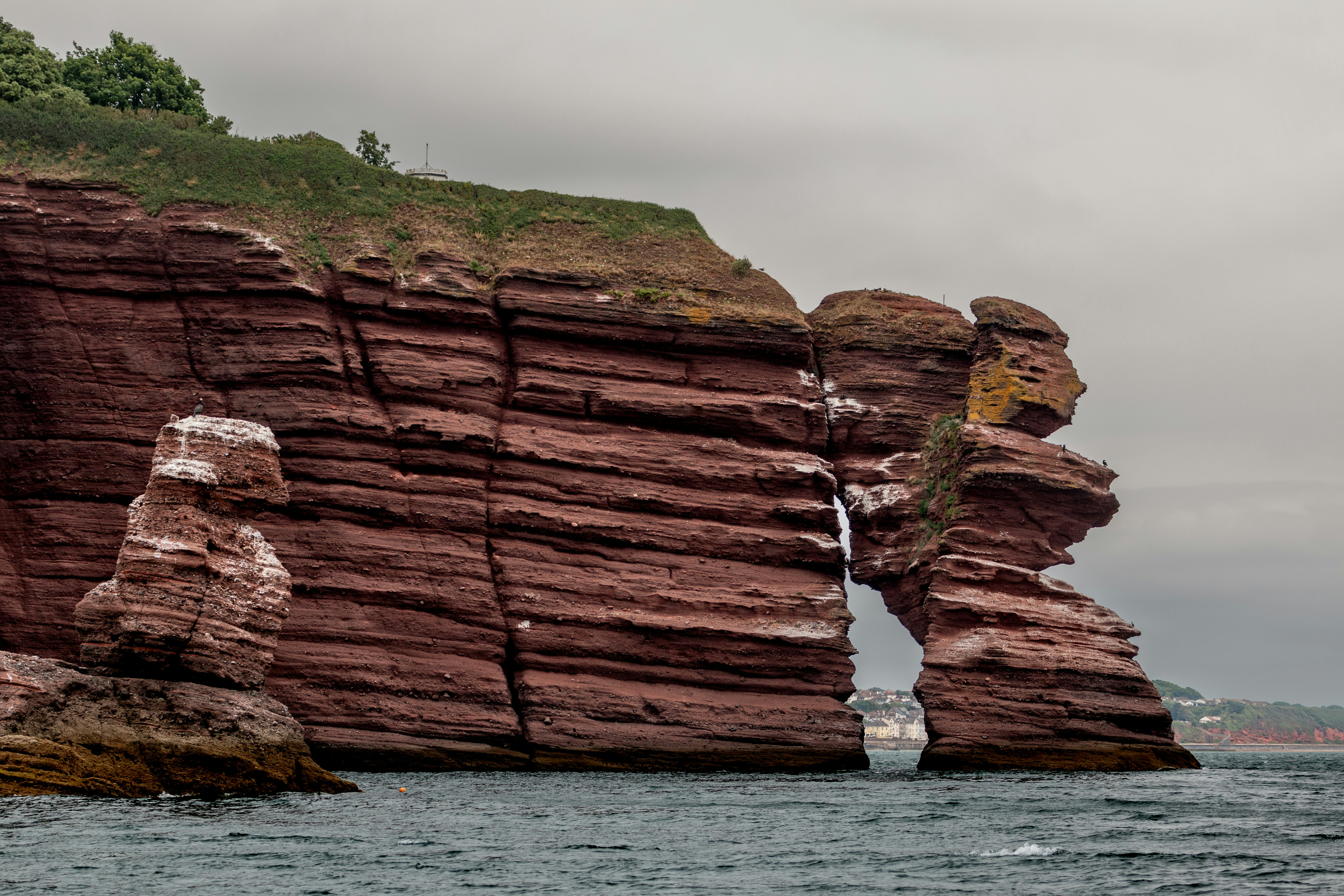 Layered red cliffs rise majestically above the sea under a cloudy sky.
