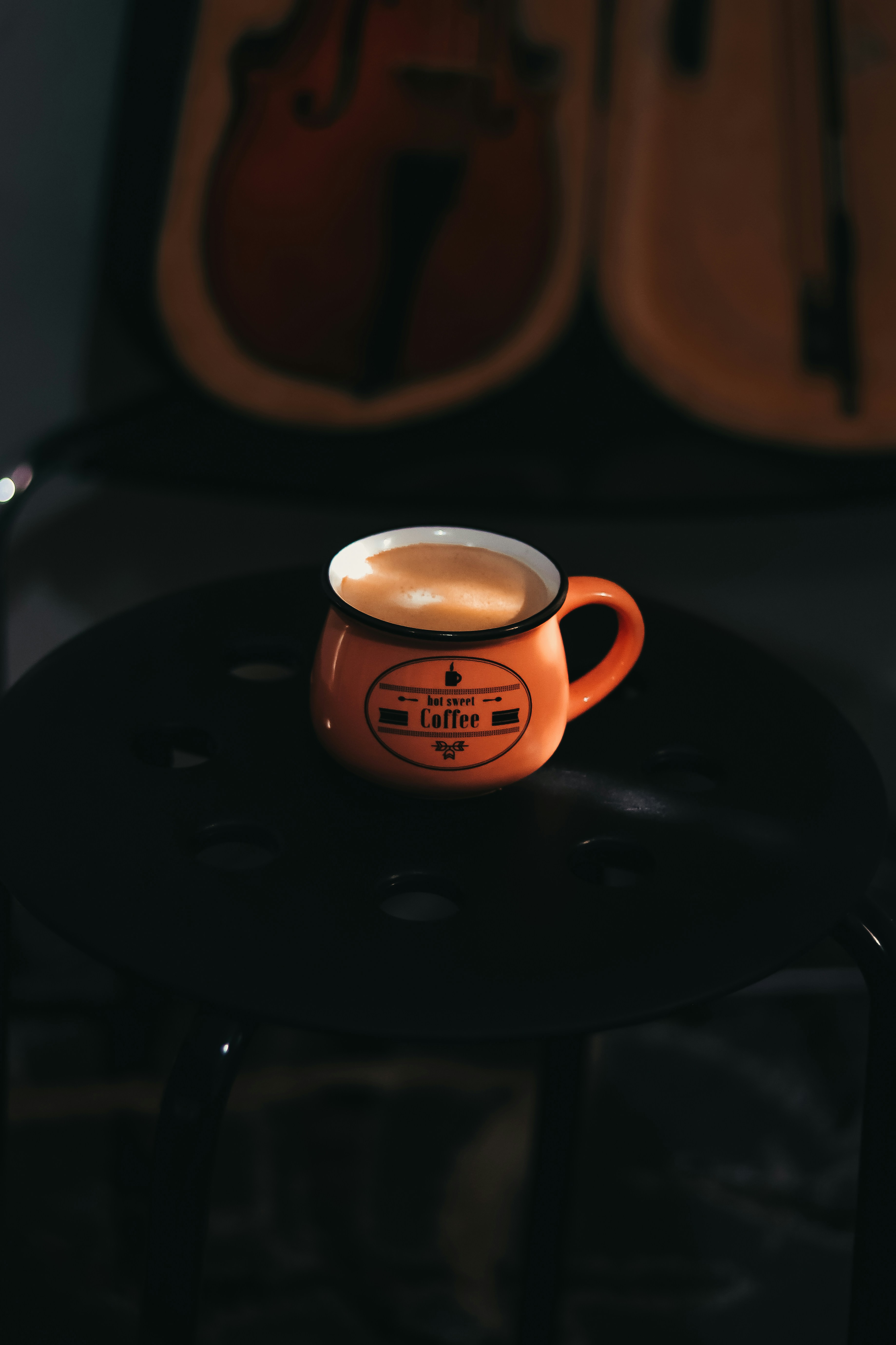 Tiny Orange Coffee Cup on a Black Stool with Guitar Case Backdrop