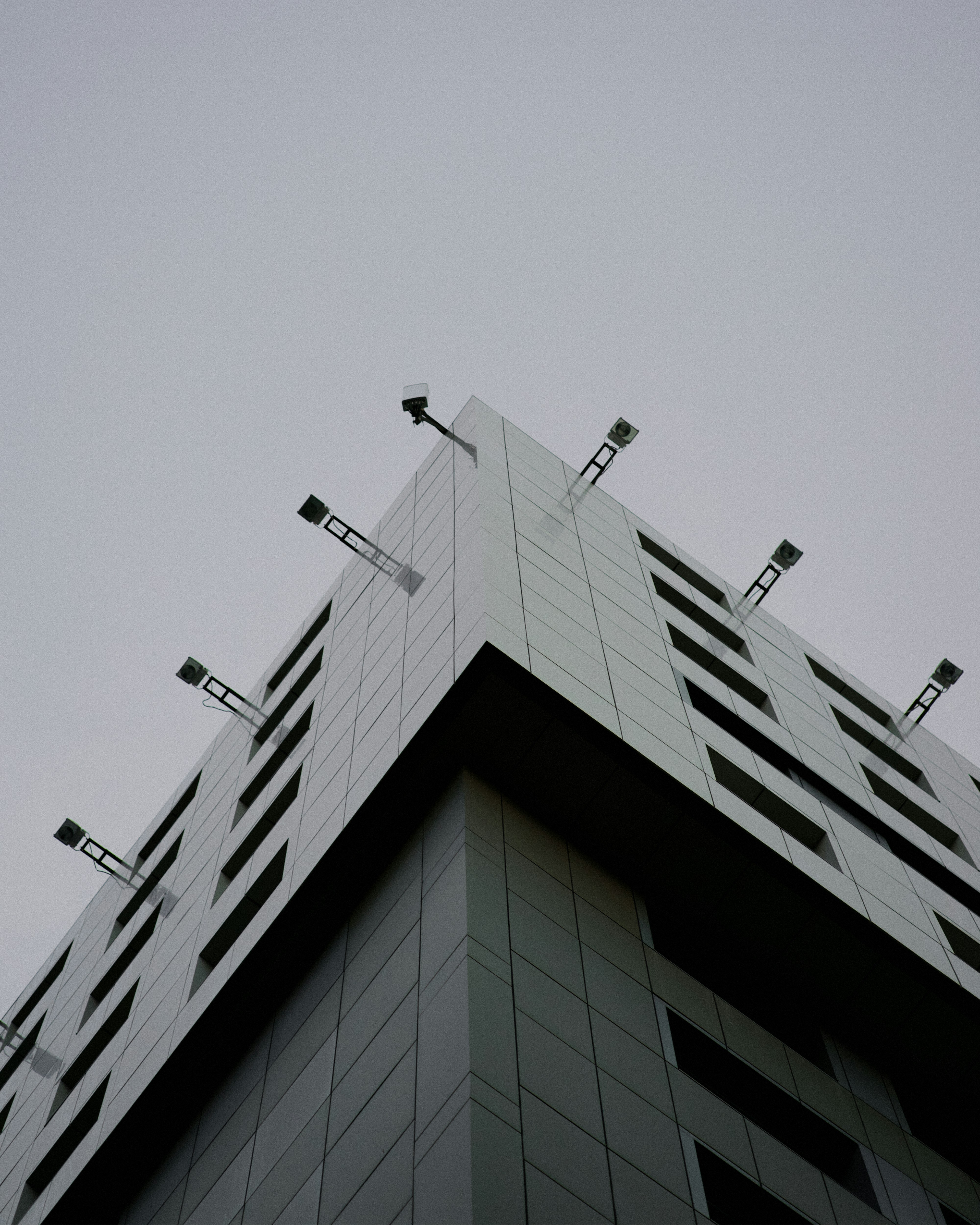 A towering modern building captured from a low angle, showcasing its sleek lines and security cameras on the roof.