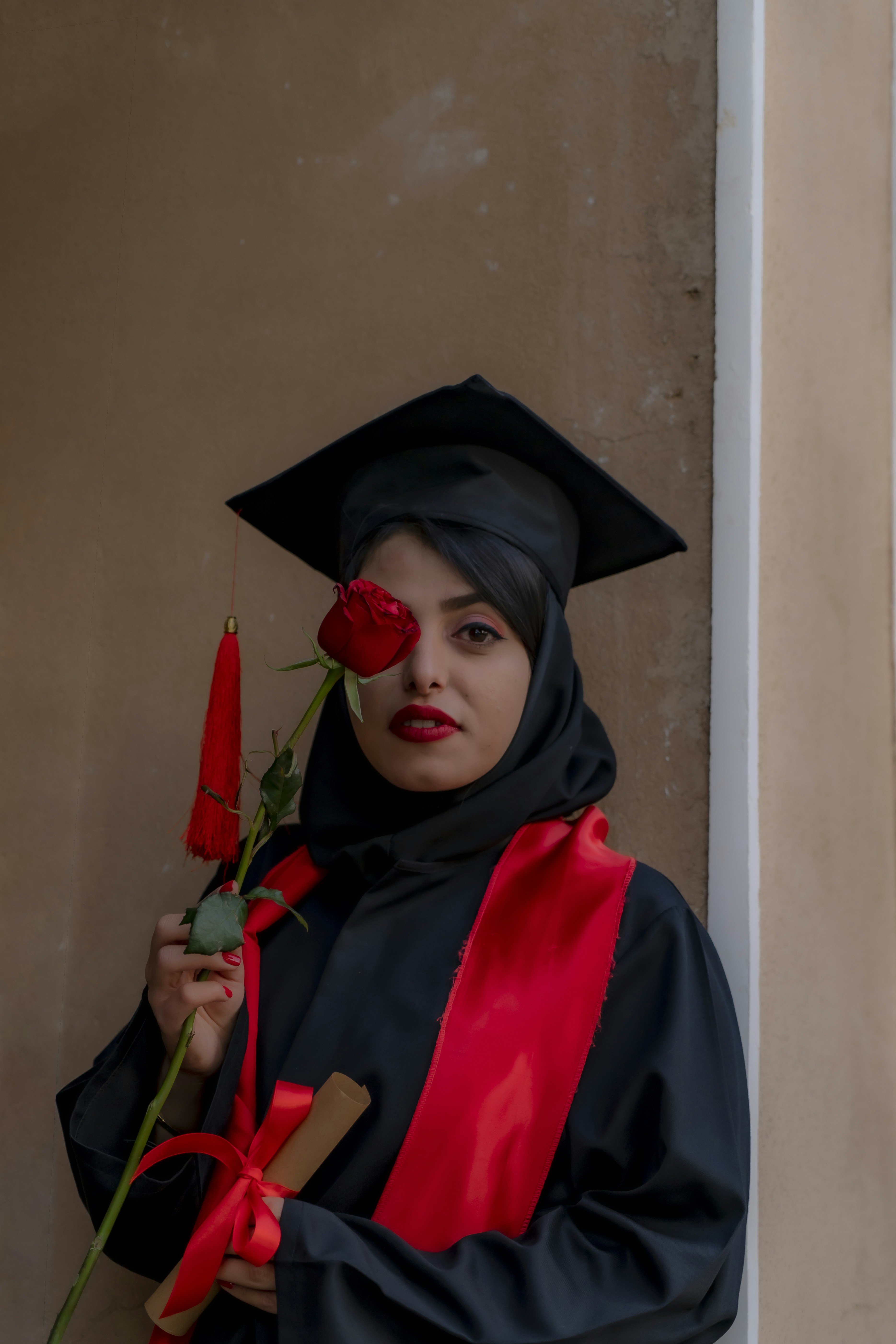A person wearing a graduation cap and gown holding a red rose photo ...