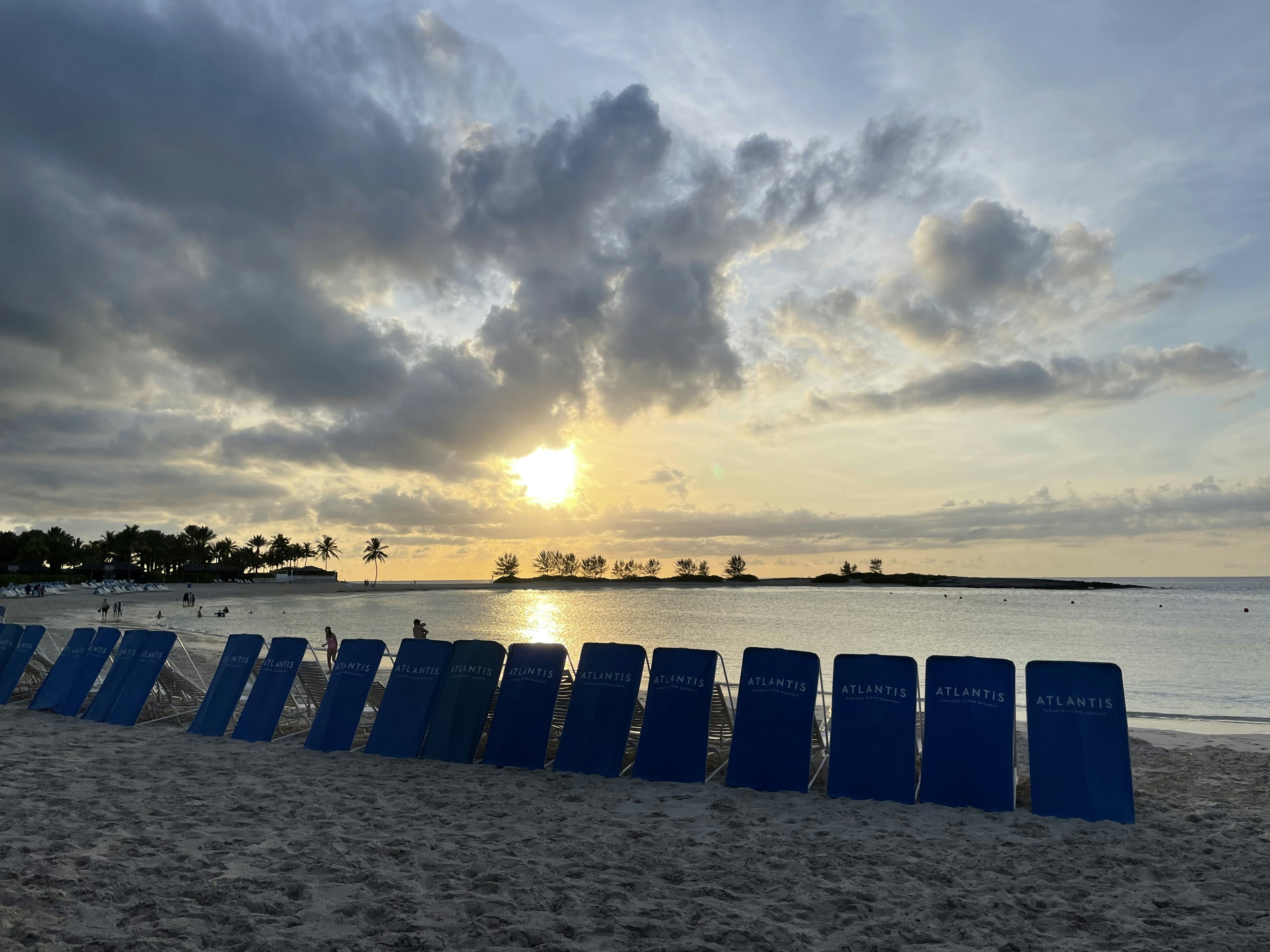 Beach chairs lined up on sandy shore, overlooking a tranquil sea and a setting sun. The scene captures the essence of relaxation and coastal beauty.
