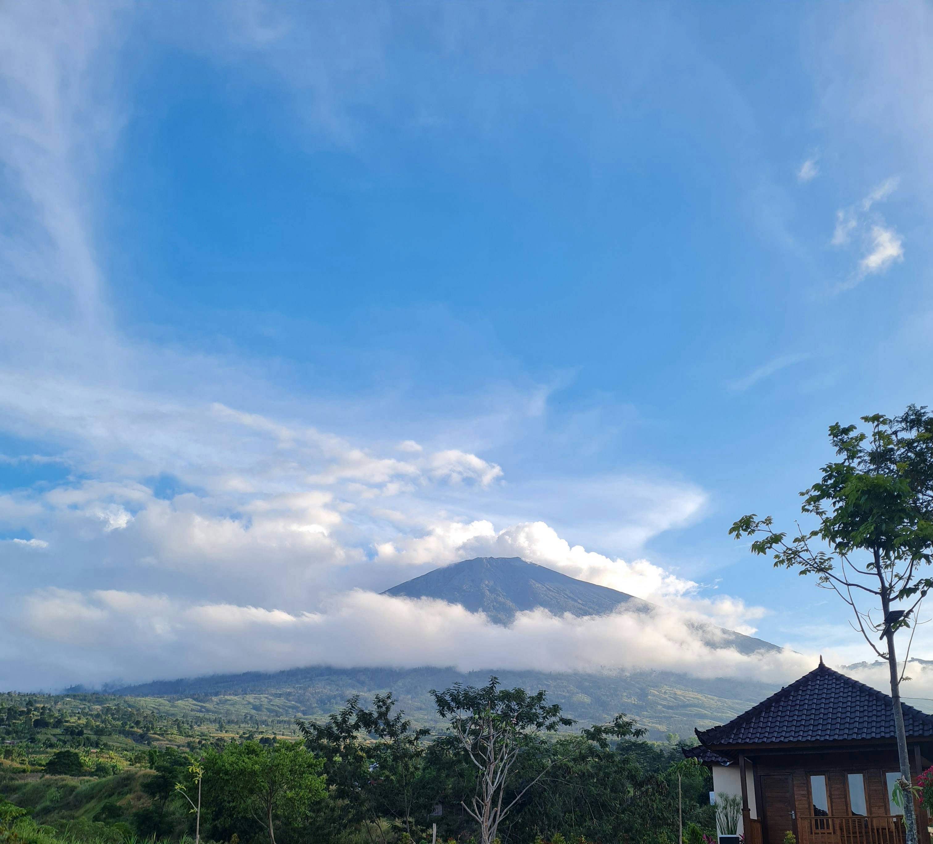 Distant mountain peaks rise above lush greenery and a small building under a clear blue sky.