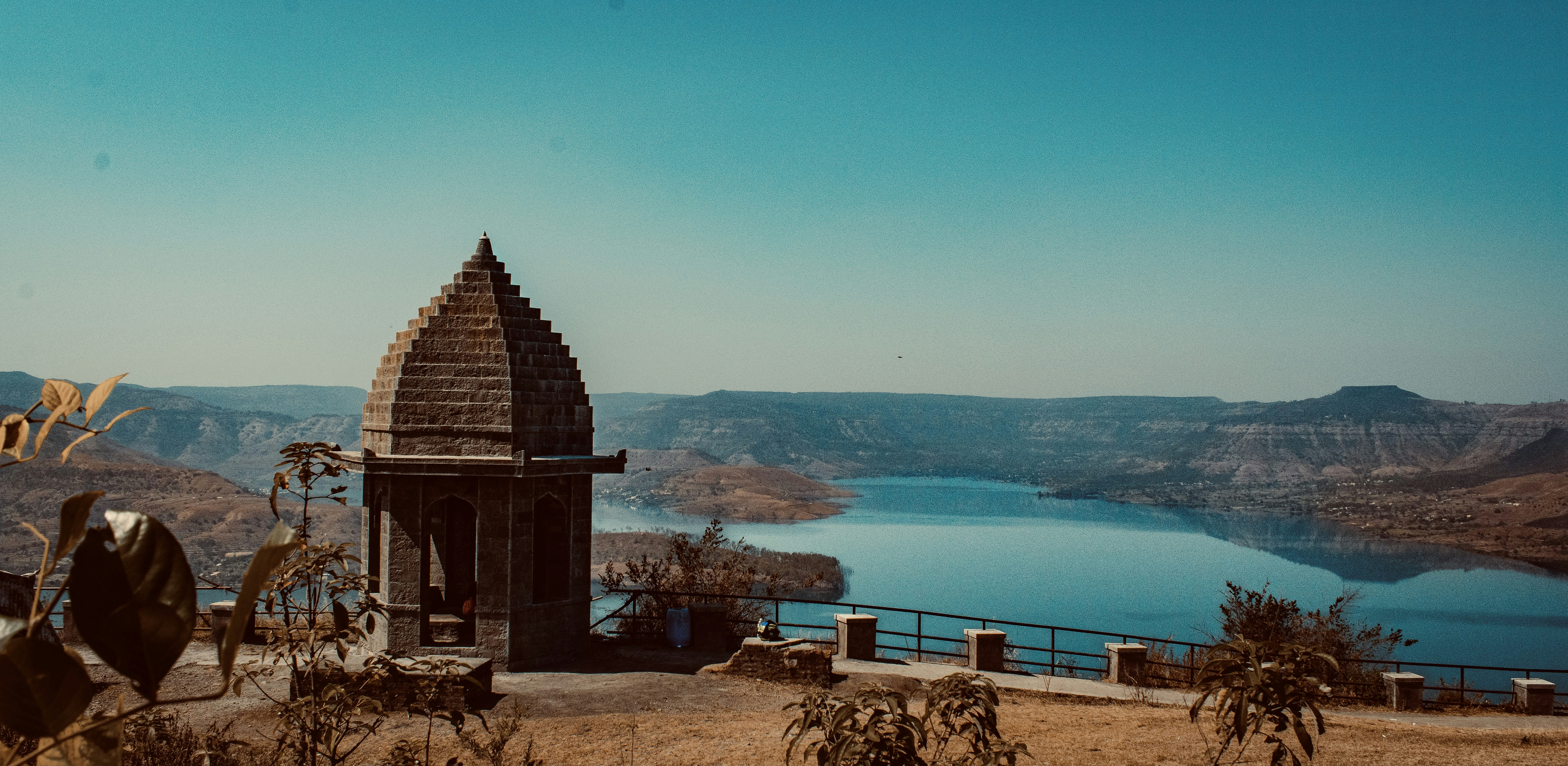 A stone tower stands on a hilltop with a vast blue lake and distant mountains in the background.