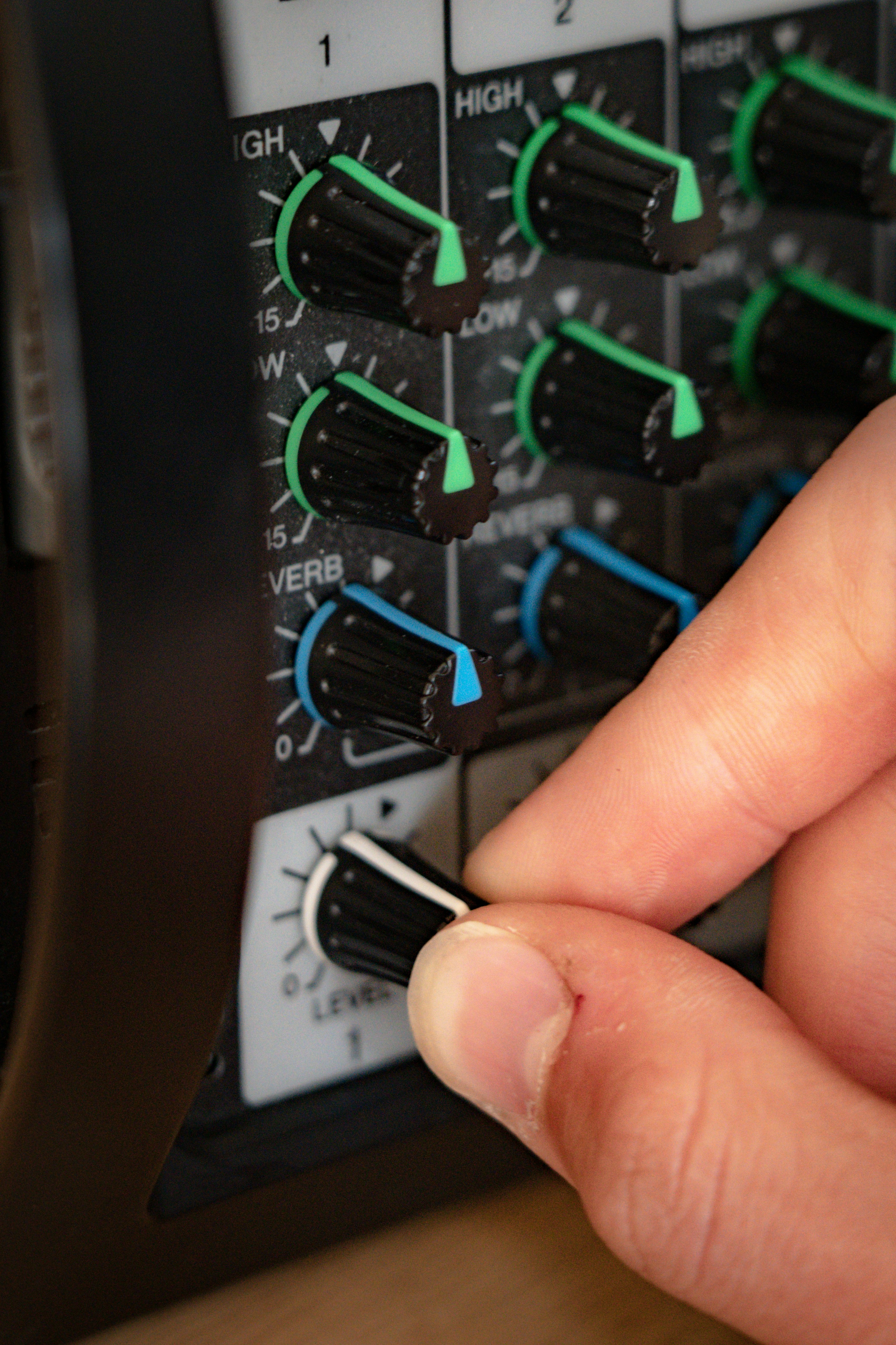 Hand adjusting the level control on an audio mixer, showcasing various knobs and settings for sound modulation.