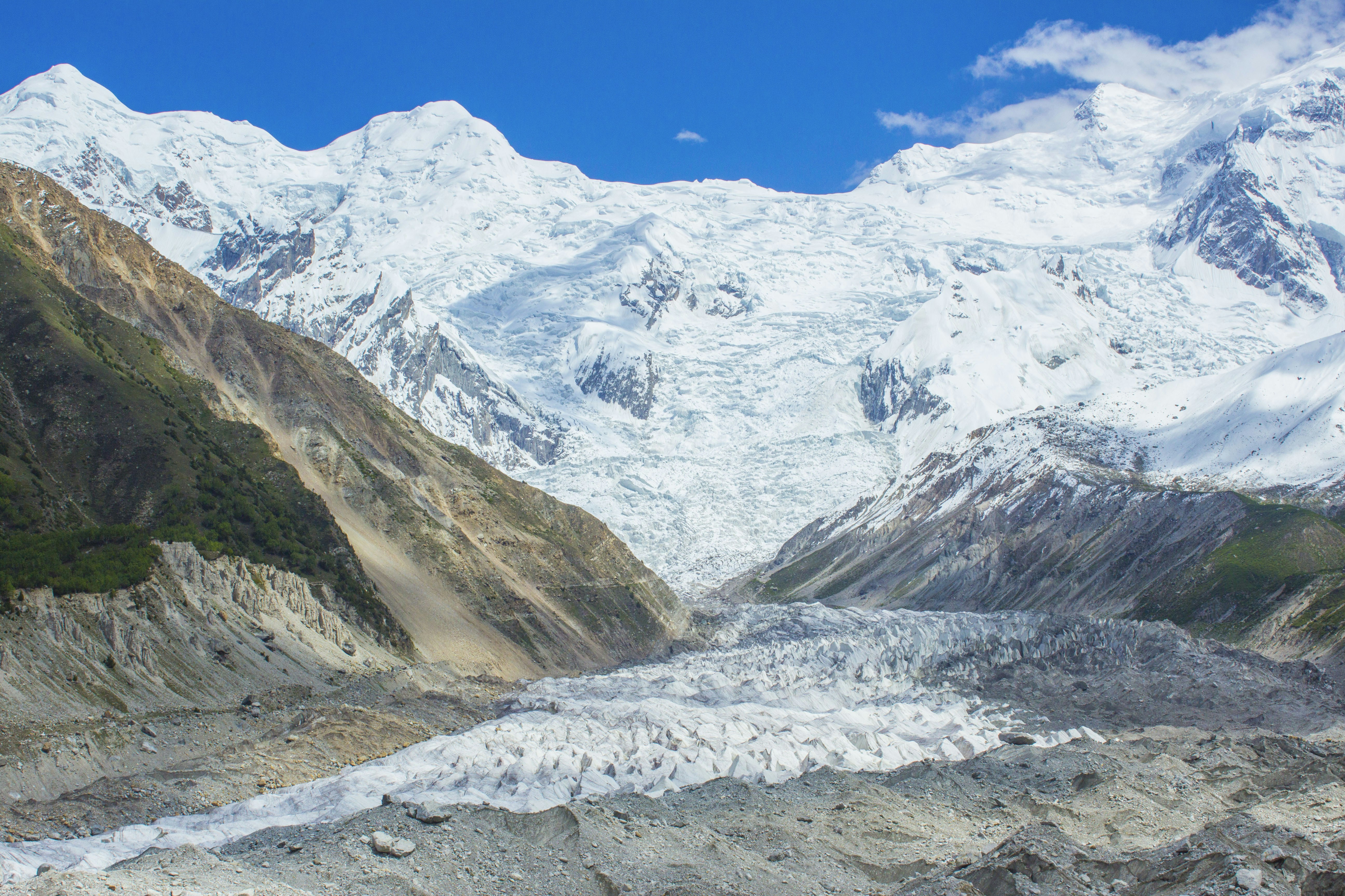 Snow-capped mountain range with a glacier extending into a rocky valley under a clear blue sky.