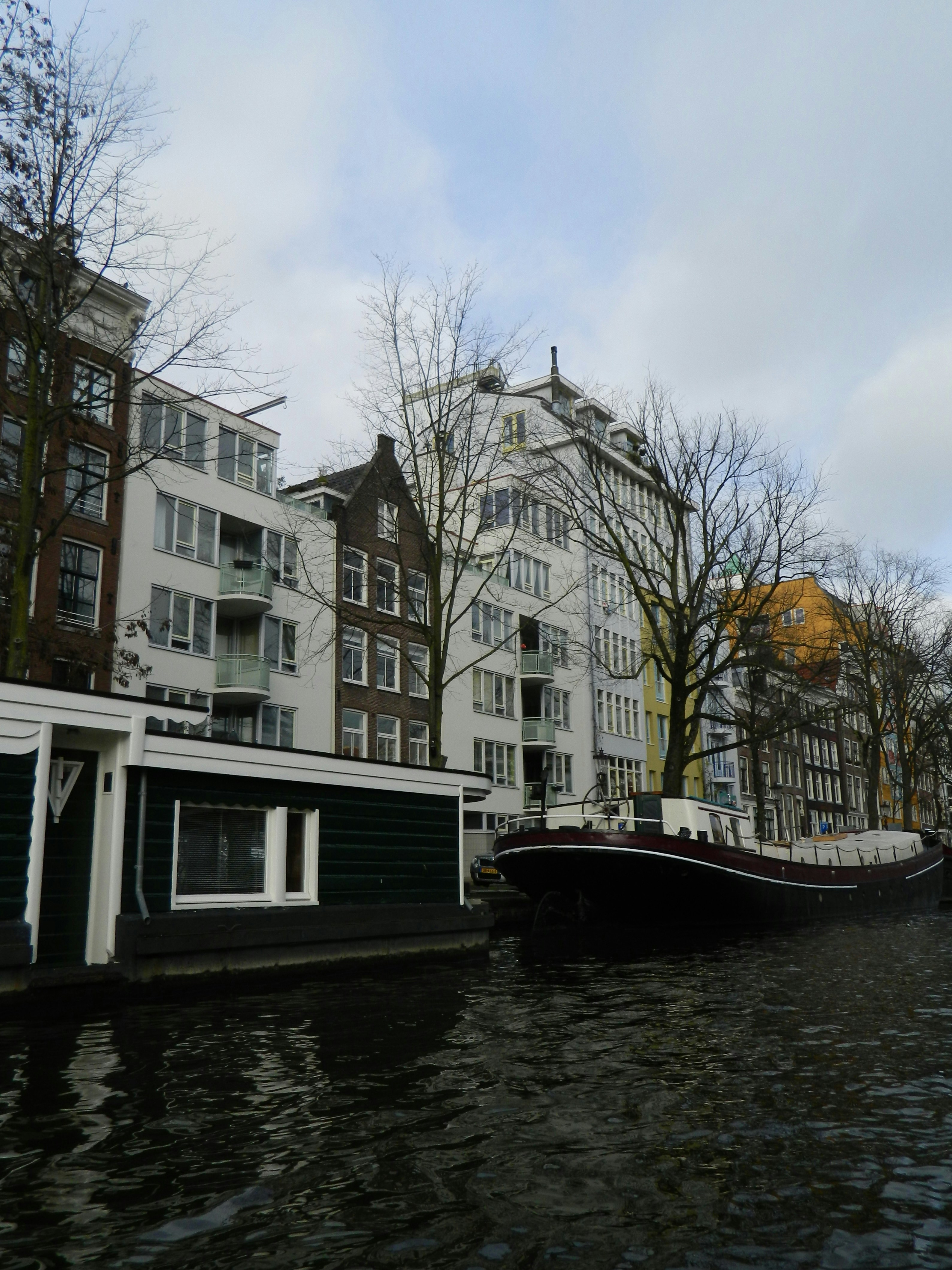 Charming canal-side buildings framed by bare trees, with a vintage boat moored peacefully in the water.