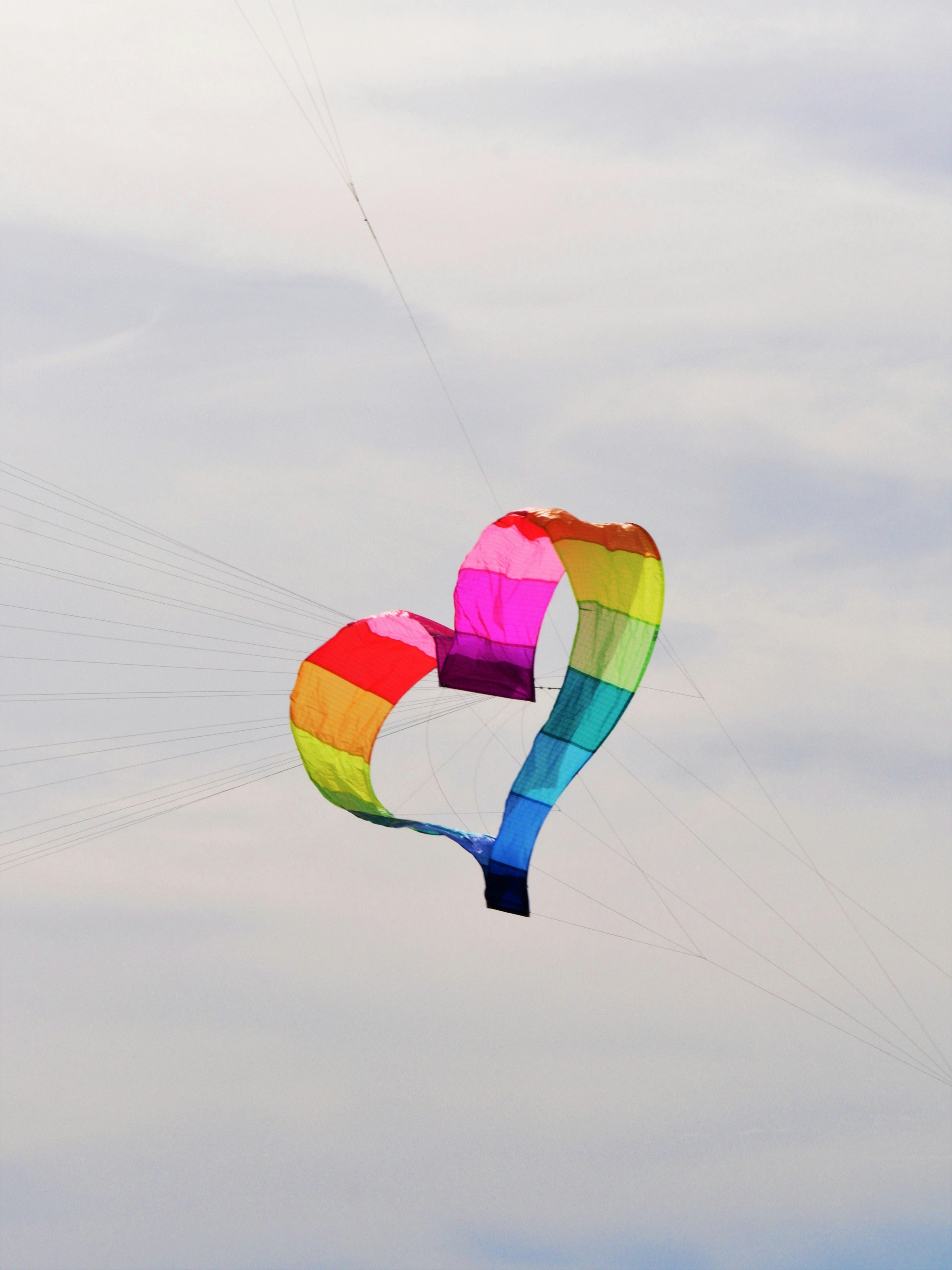 Colorful heart-shaped kite soaring against a cloudy backdrop, showcasing vibrant hues of red, pink, yellow, and blue.