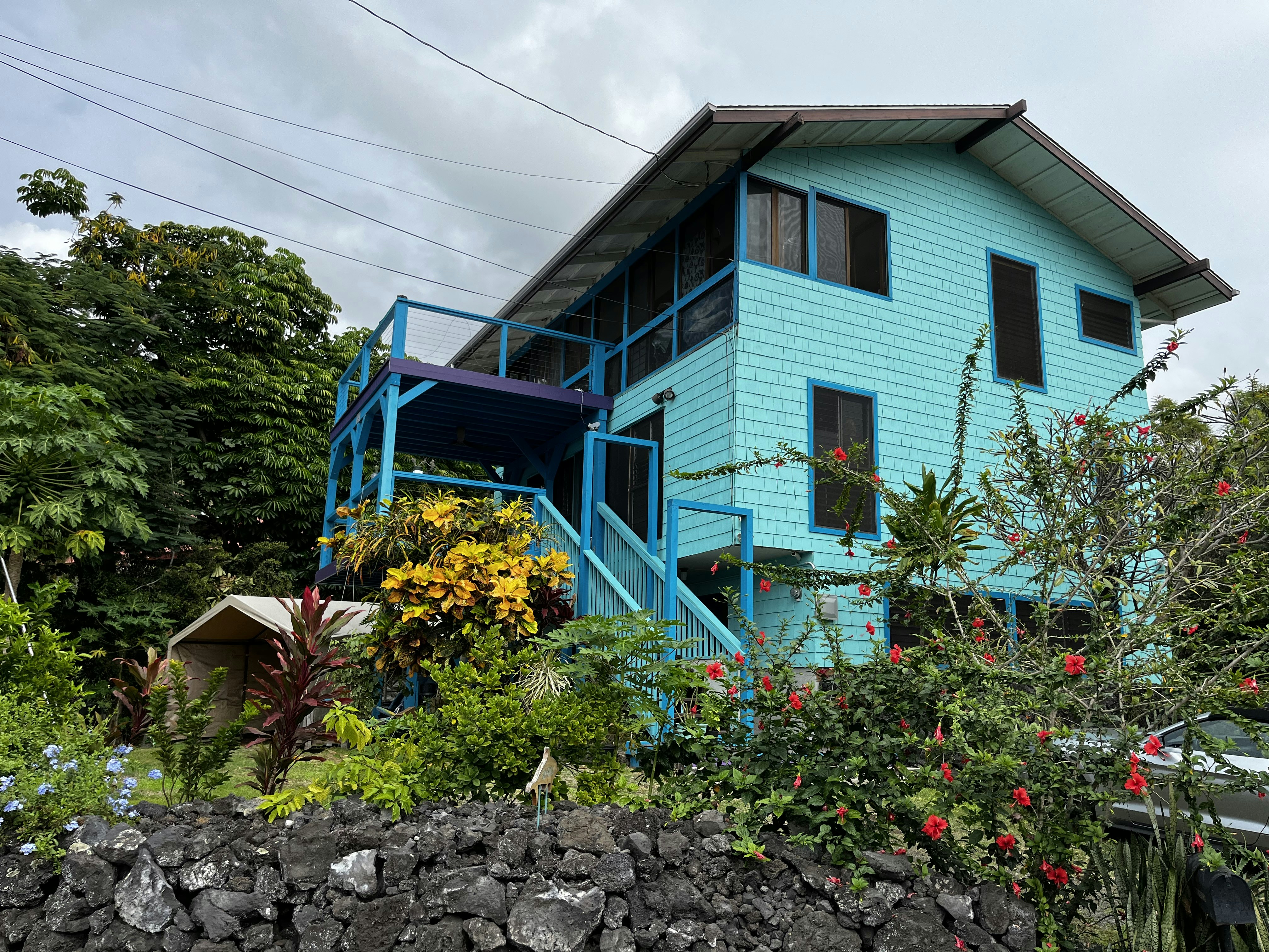 Colorful two-story house surrounded by tropical plants and flowers, showcasing a blend of architecture with nature's beauty.