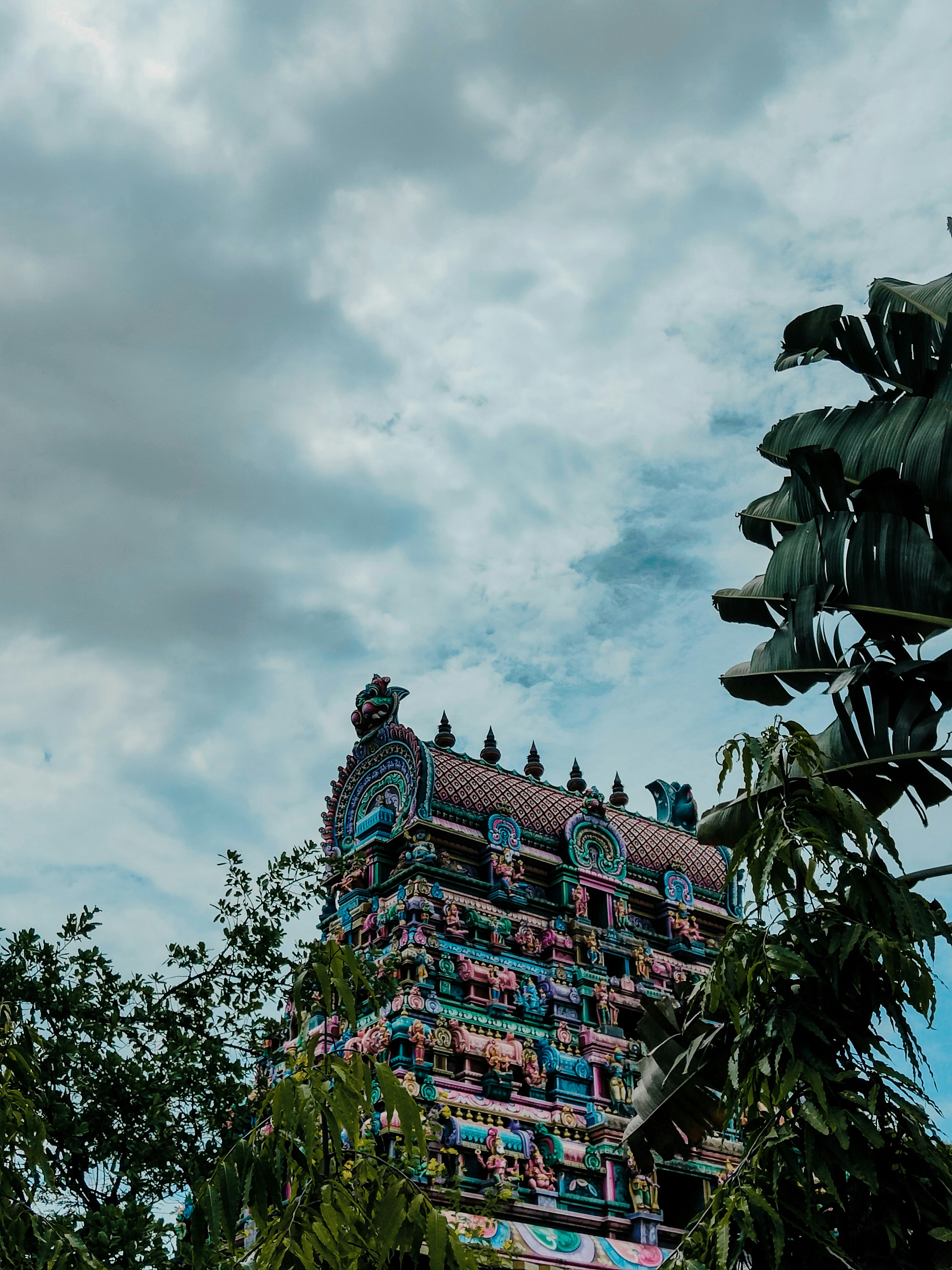 Colorful temple tower peeking through tropical greenery under a bright sky