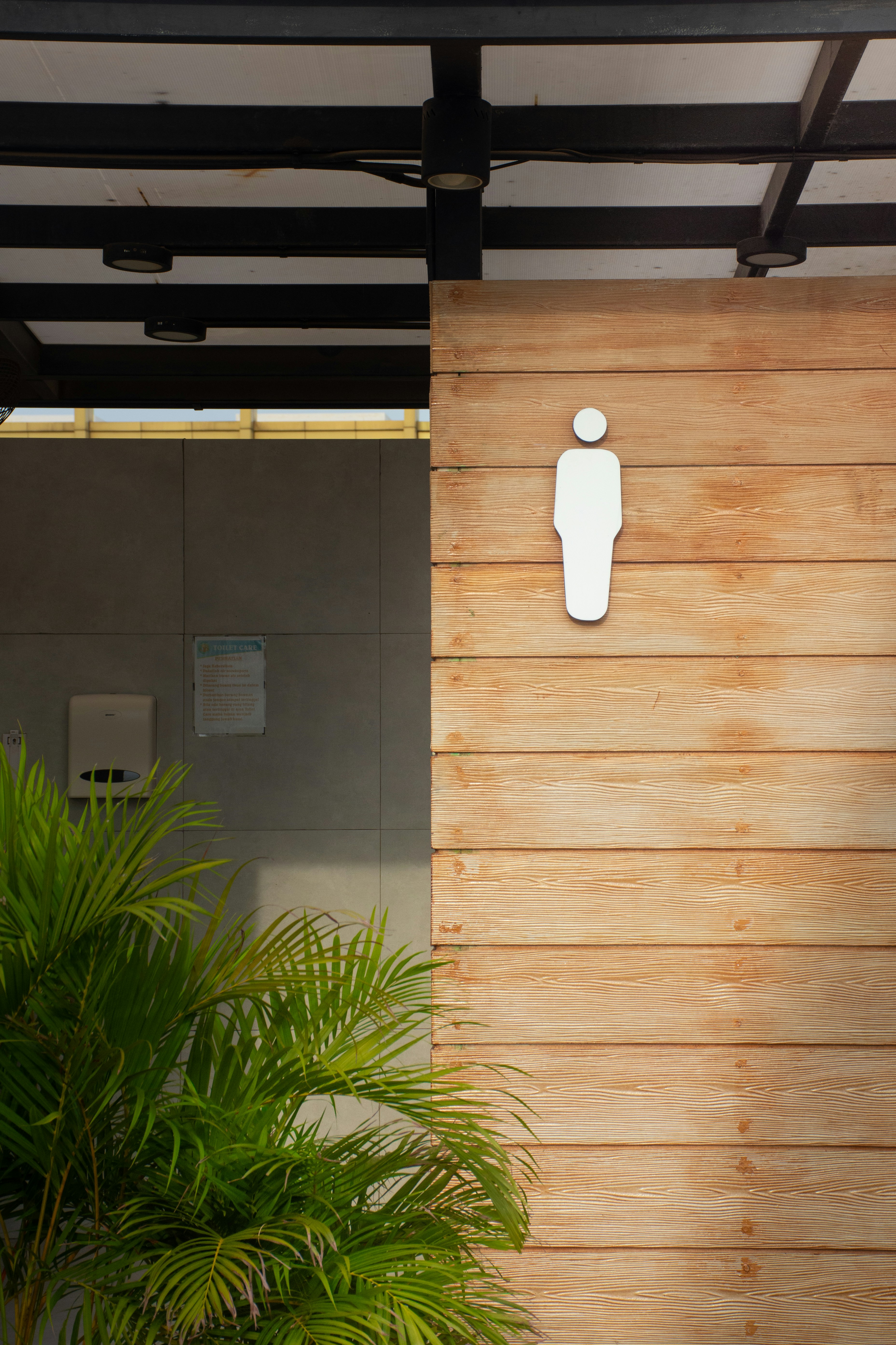 Wooden Partition with White Male Icon Amid Greenery and Modern Ceiling