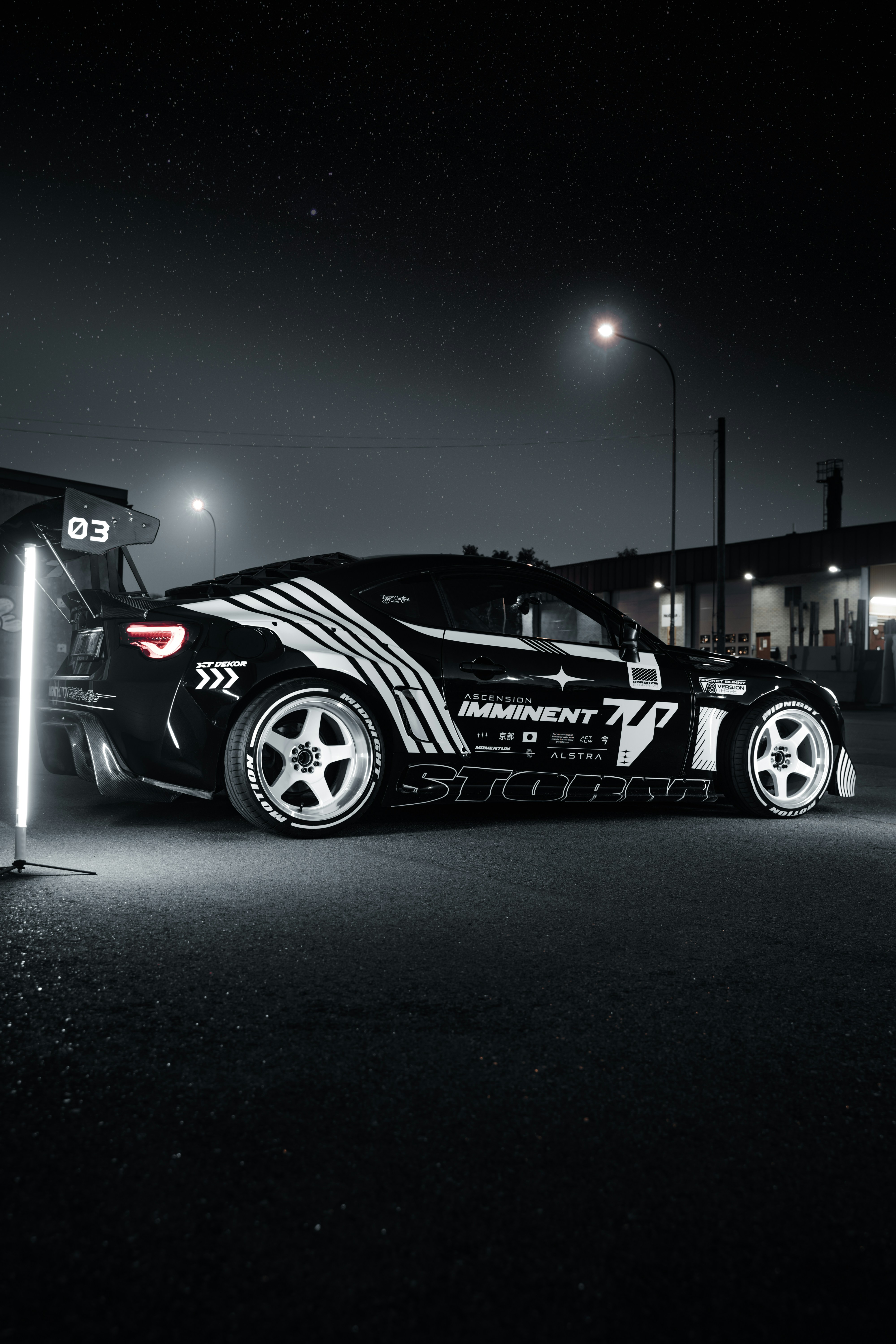 Black sports car with bold decals illuminated under streetlights against a starry night sky.