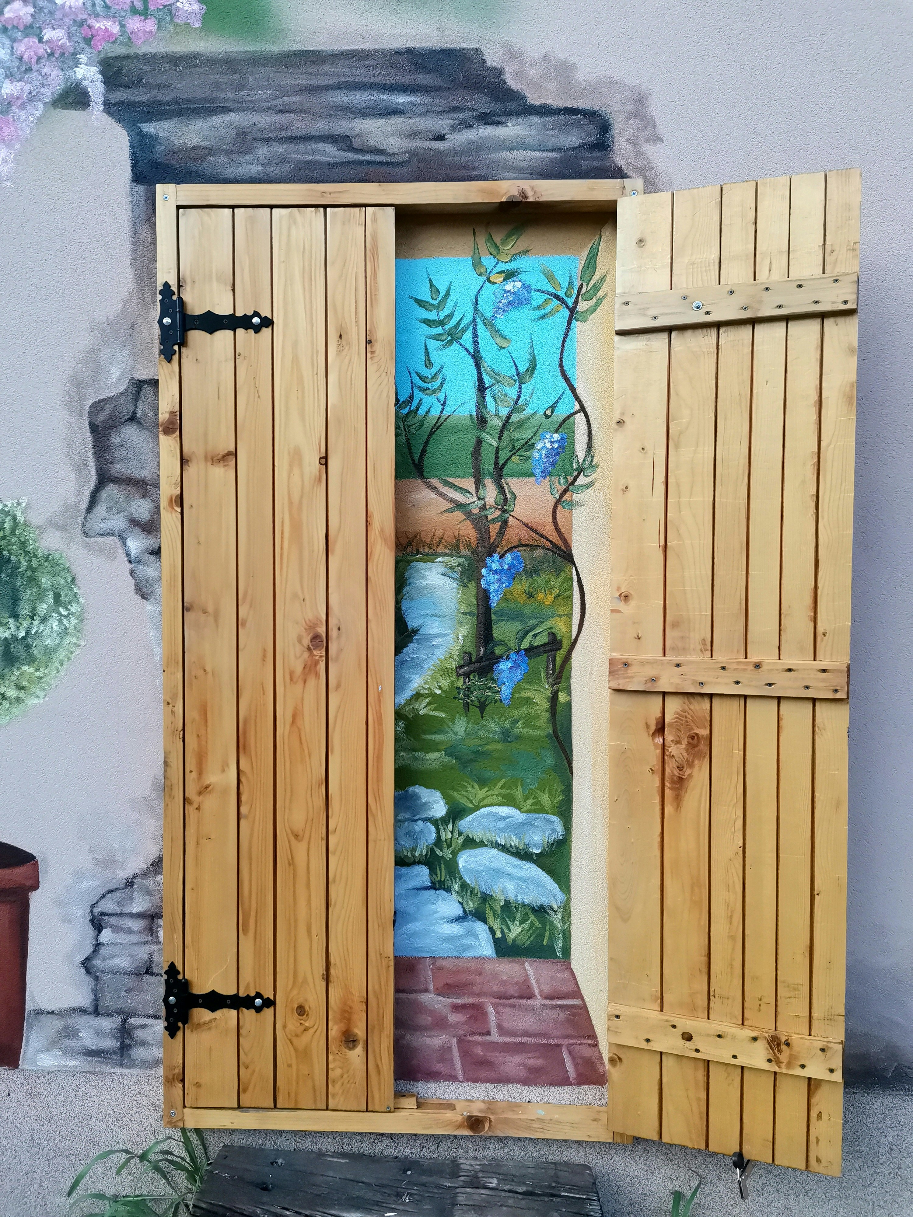 Wooden shutters opened to reveal a vibrant mural depicting a serene landscape with a river and foliage. The artwork invites viewers into a peaceful natural scene.