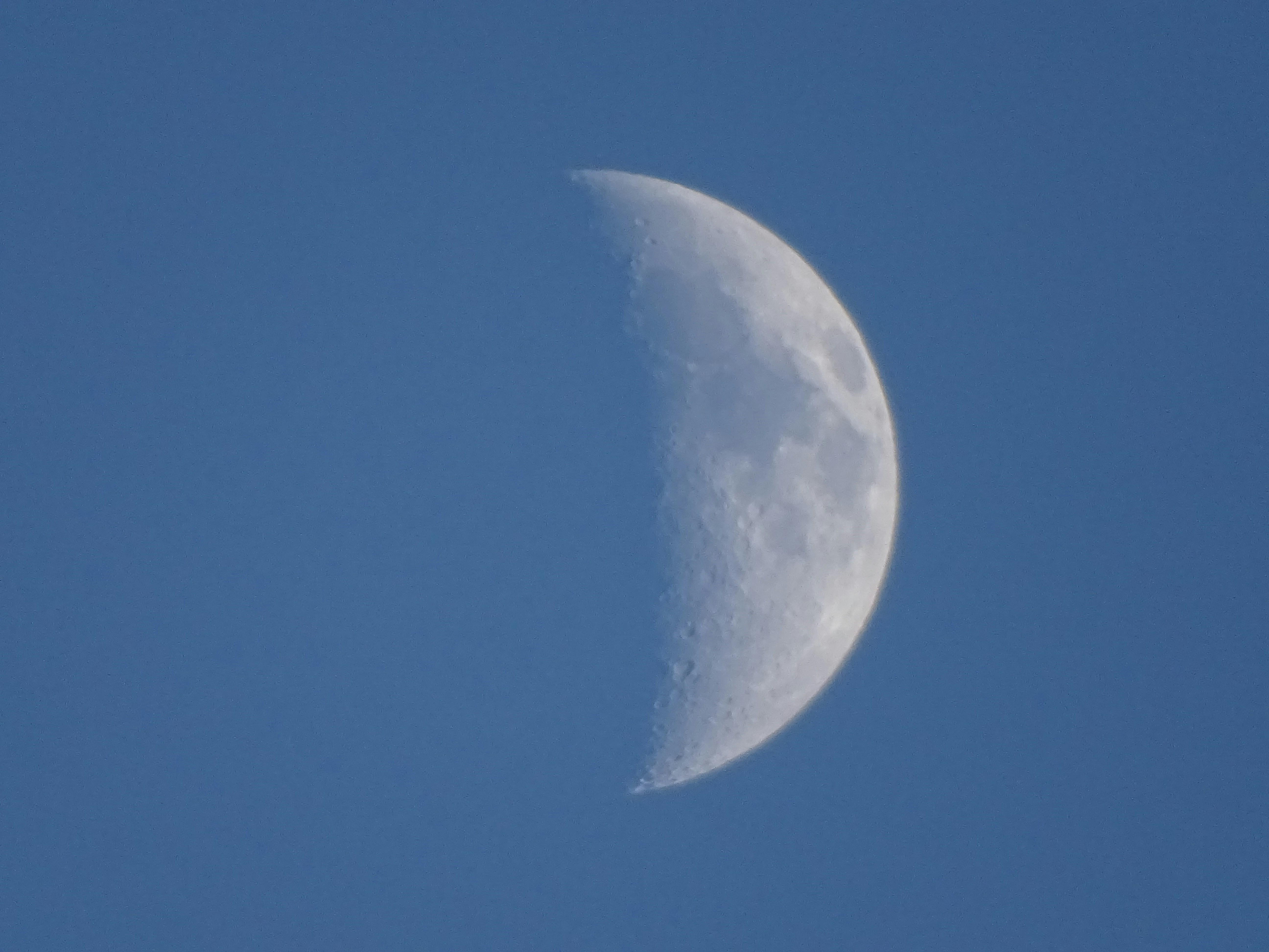 Waxing crescent moon illuminated against a clear blue sky, showcasing its delicate surface details.