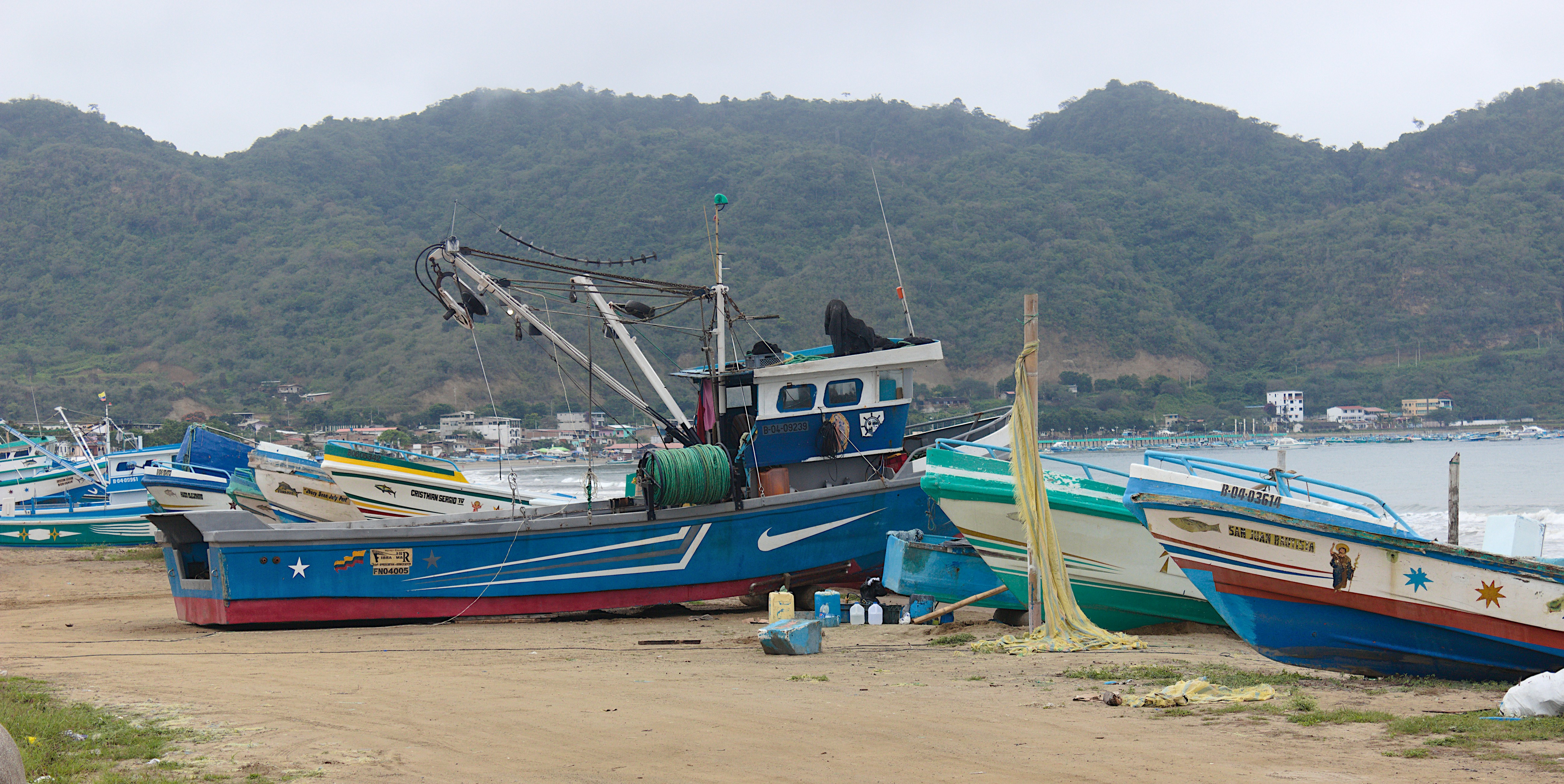 Colorful fishing boats on a sandy shore with misty hills in the background.