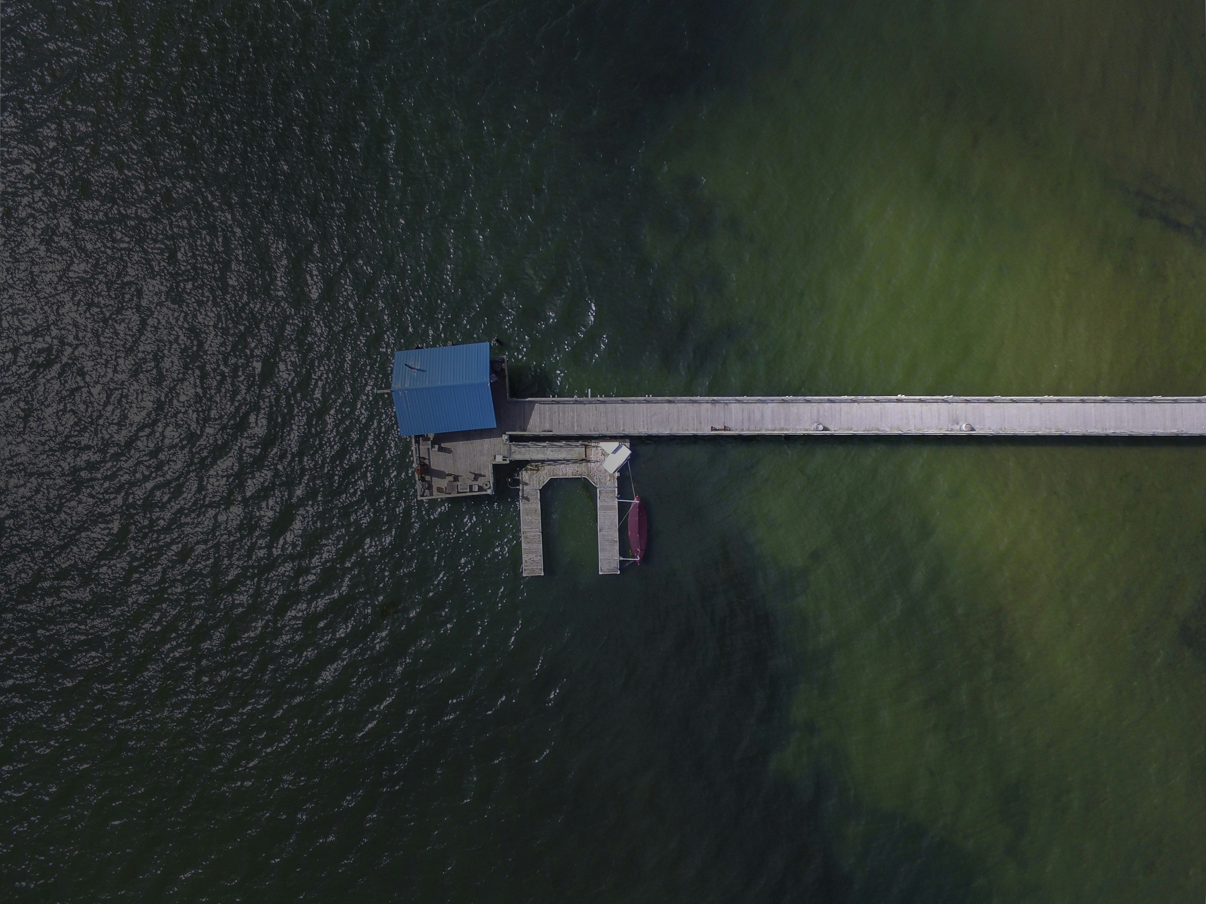 A wooden pier extends into calm waters, featuring a small blue-roofed structure at its end. The tranquil scene reflects the interplay of light on the water's surface.