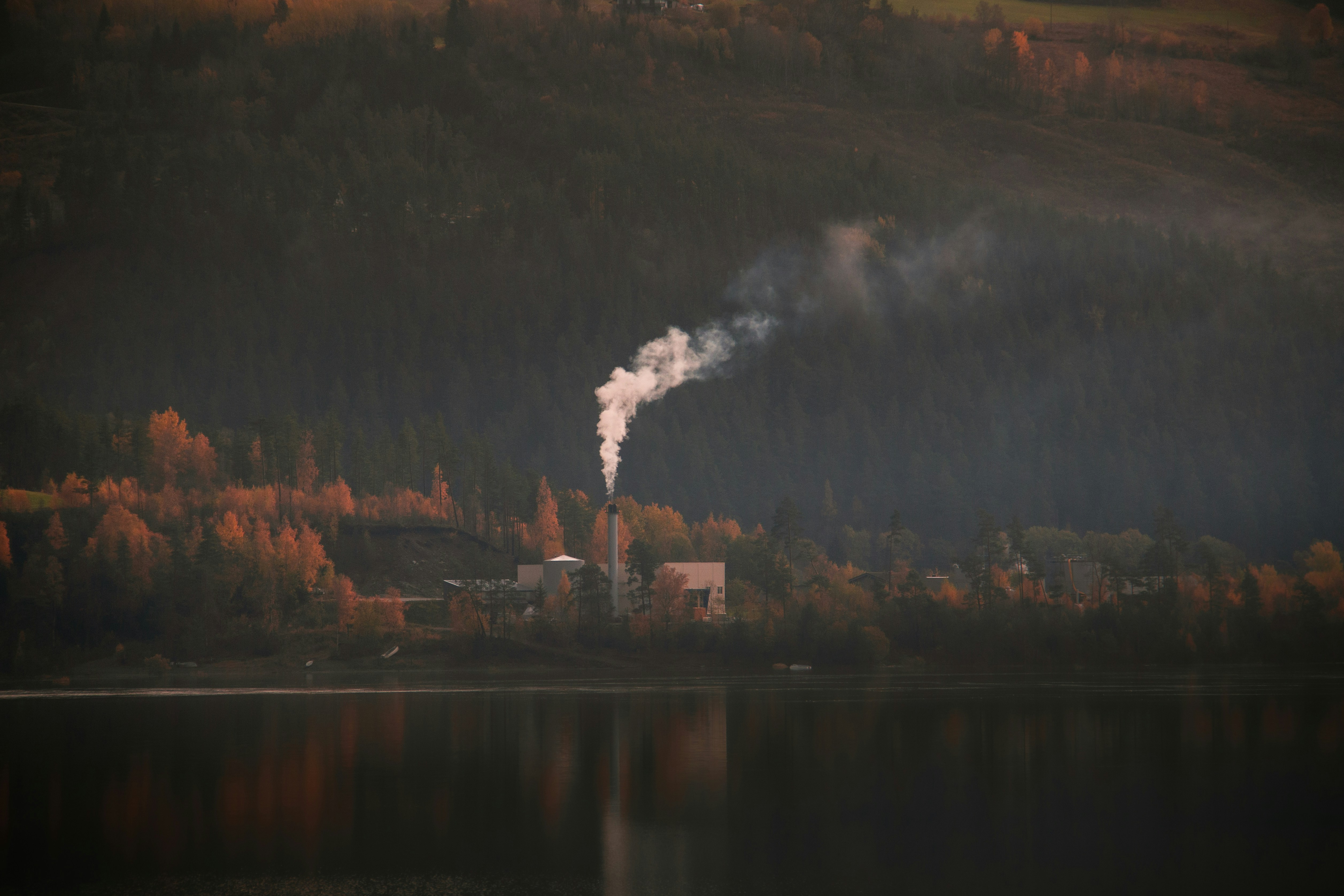 Industrial plume drifting over a tranquil lakeside at dusk