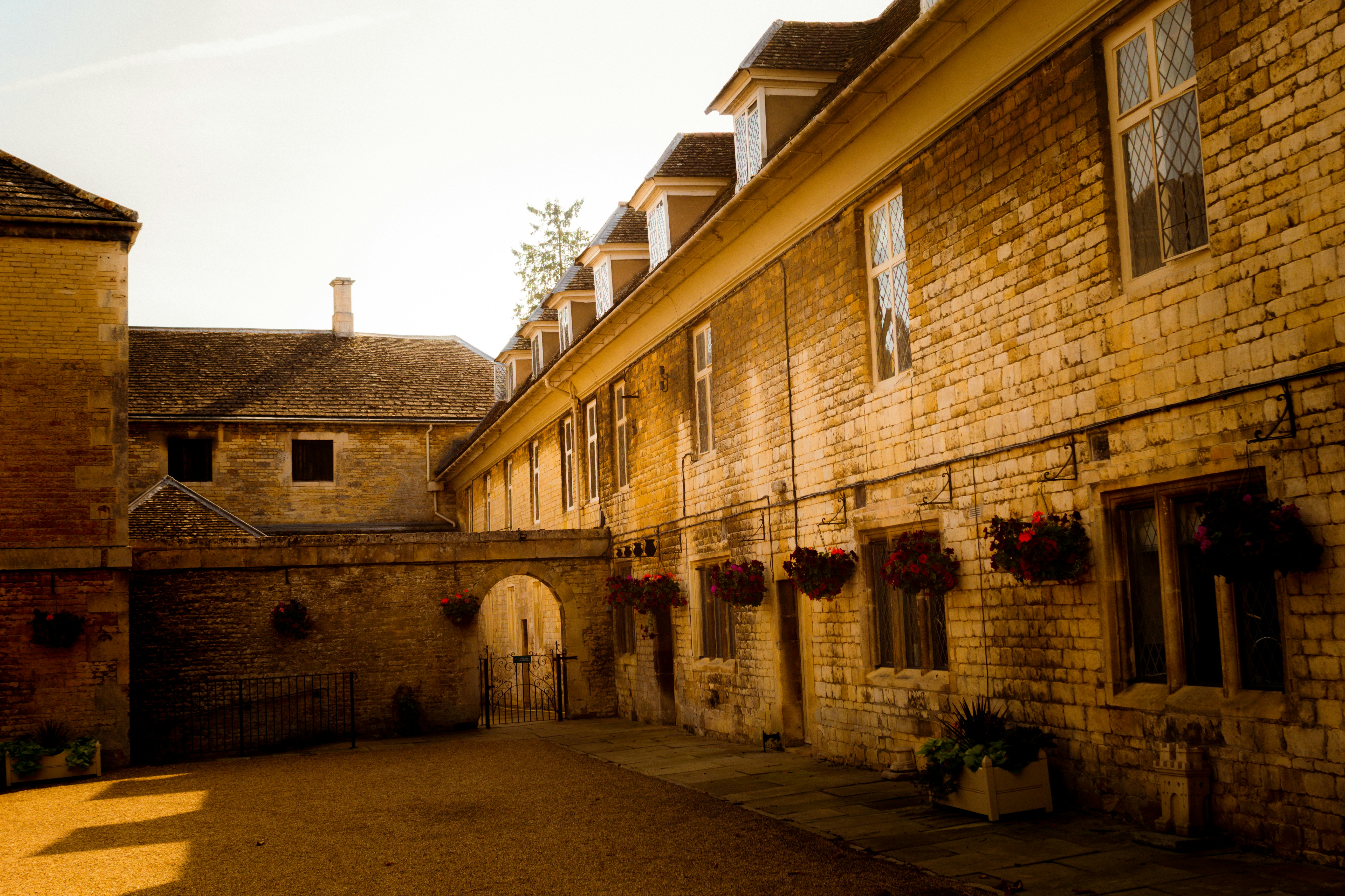 Stone manor with arched gate and hanging flower baskets bathed in warm evening light.