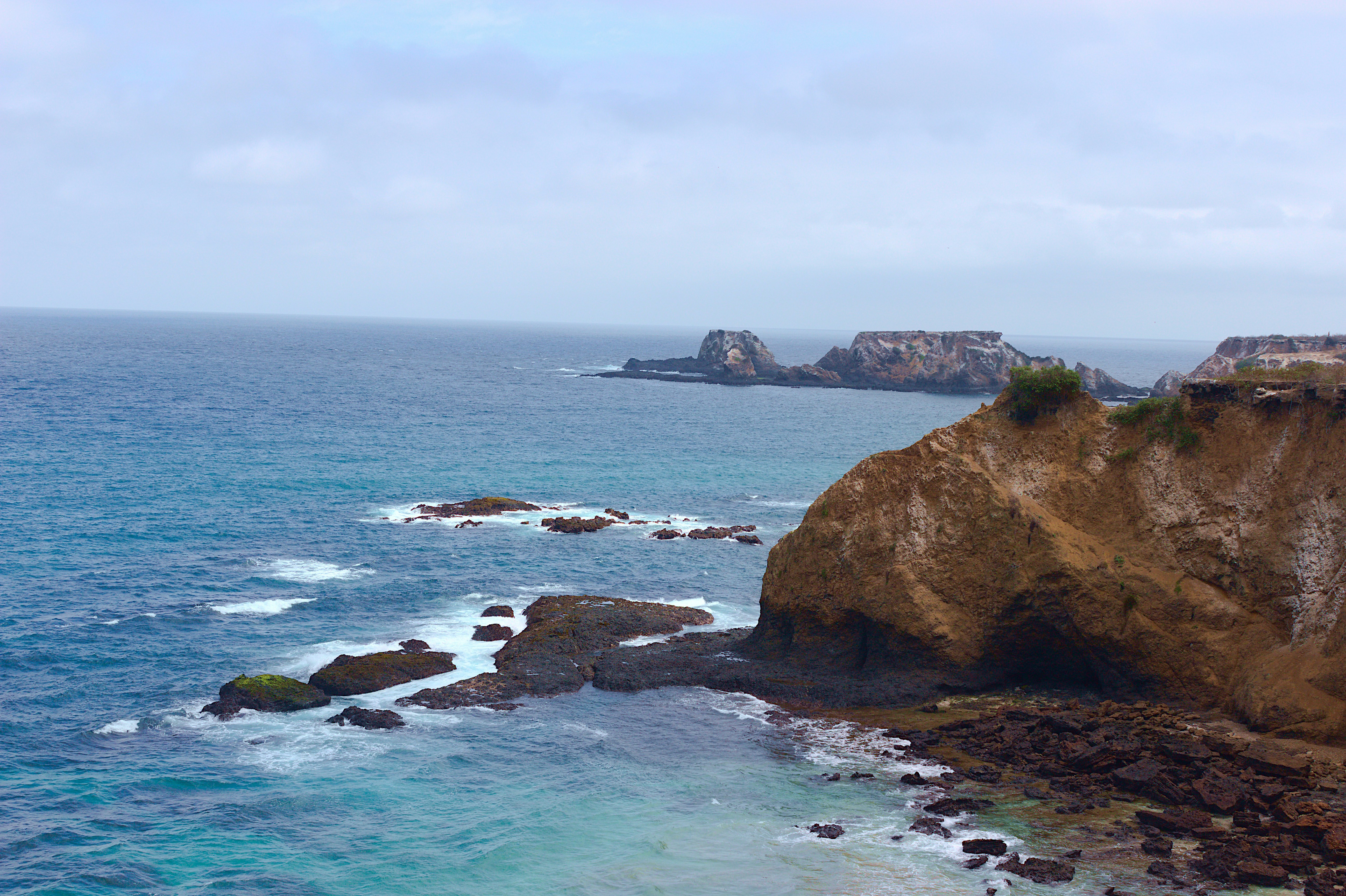 Rugged cliffs meet the tranquil ocean, with distant islands peeking through the mist. The scene captures the essence of coastal beauty.